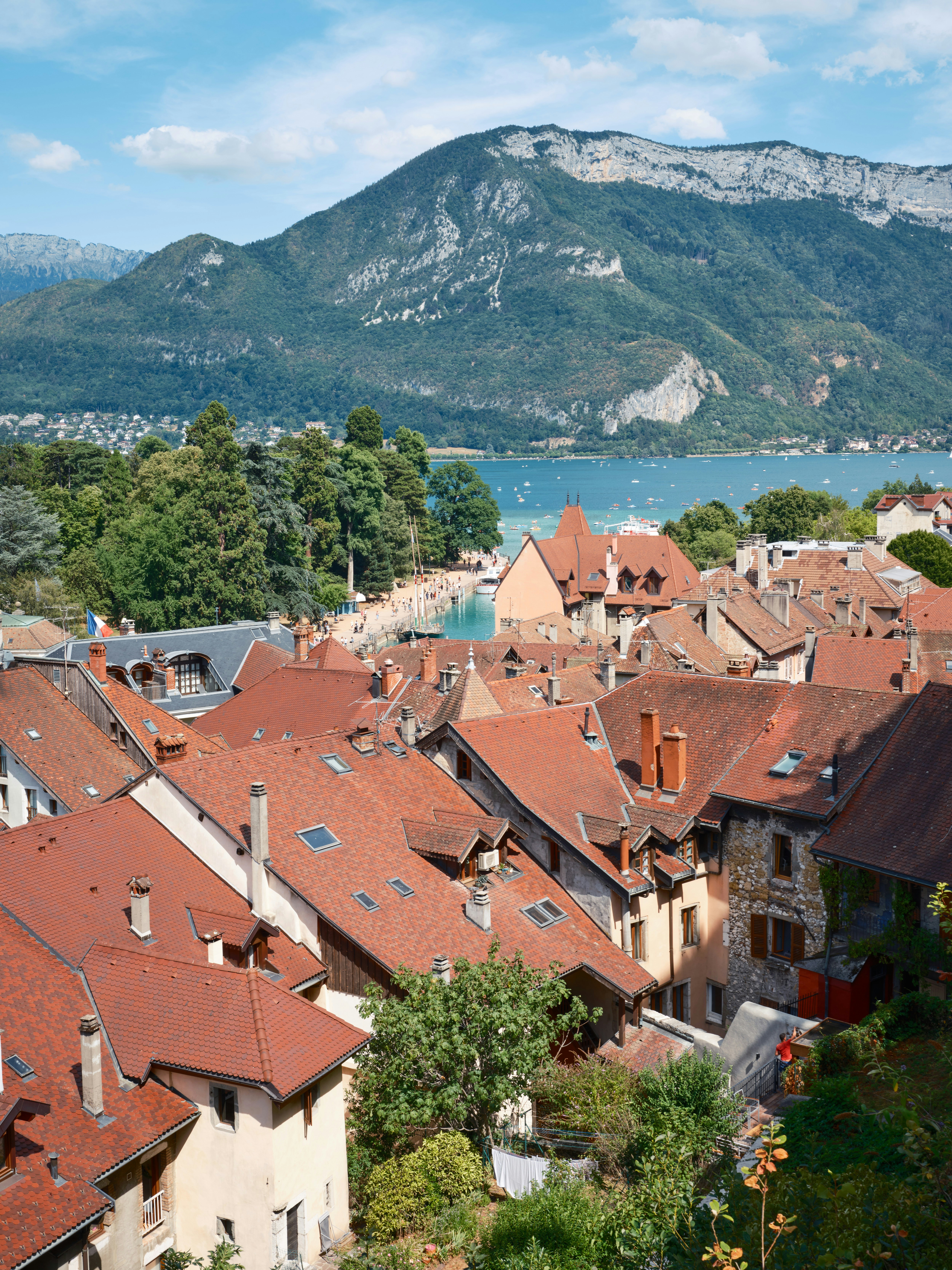 A coastal village of terracotta-tiled rooftops cascades toward a blue bay with mountains in the background.