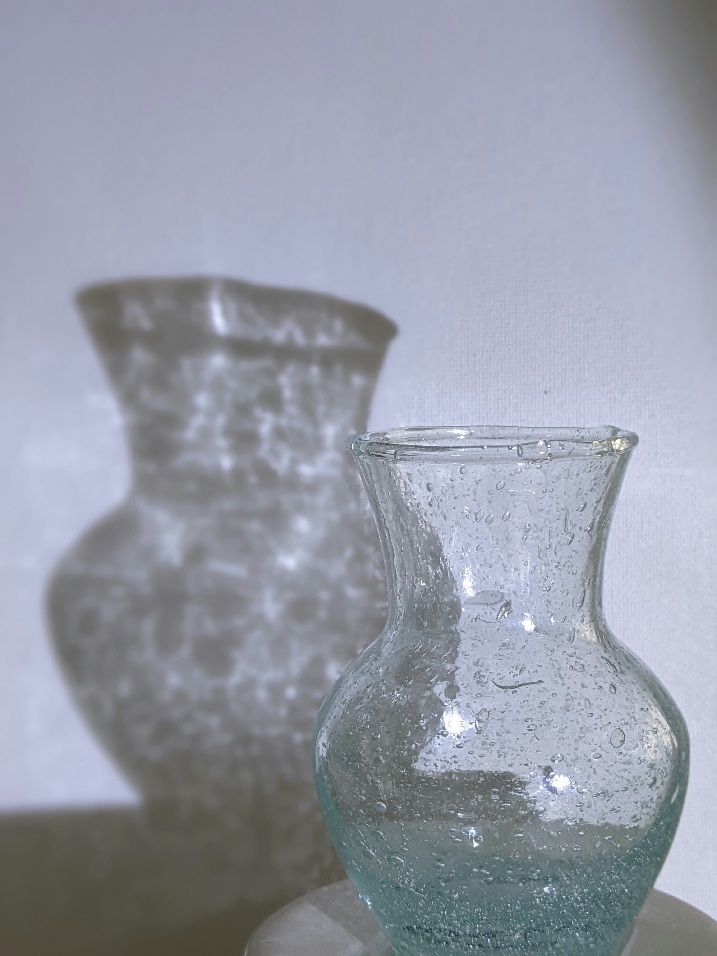 Translucent glass vase with droplets, casting a textured shadow against a light background.