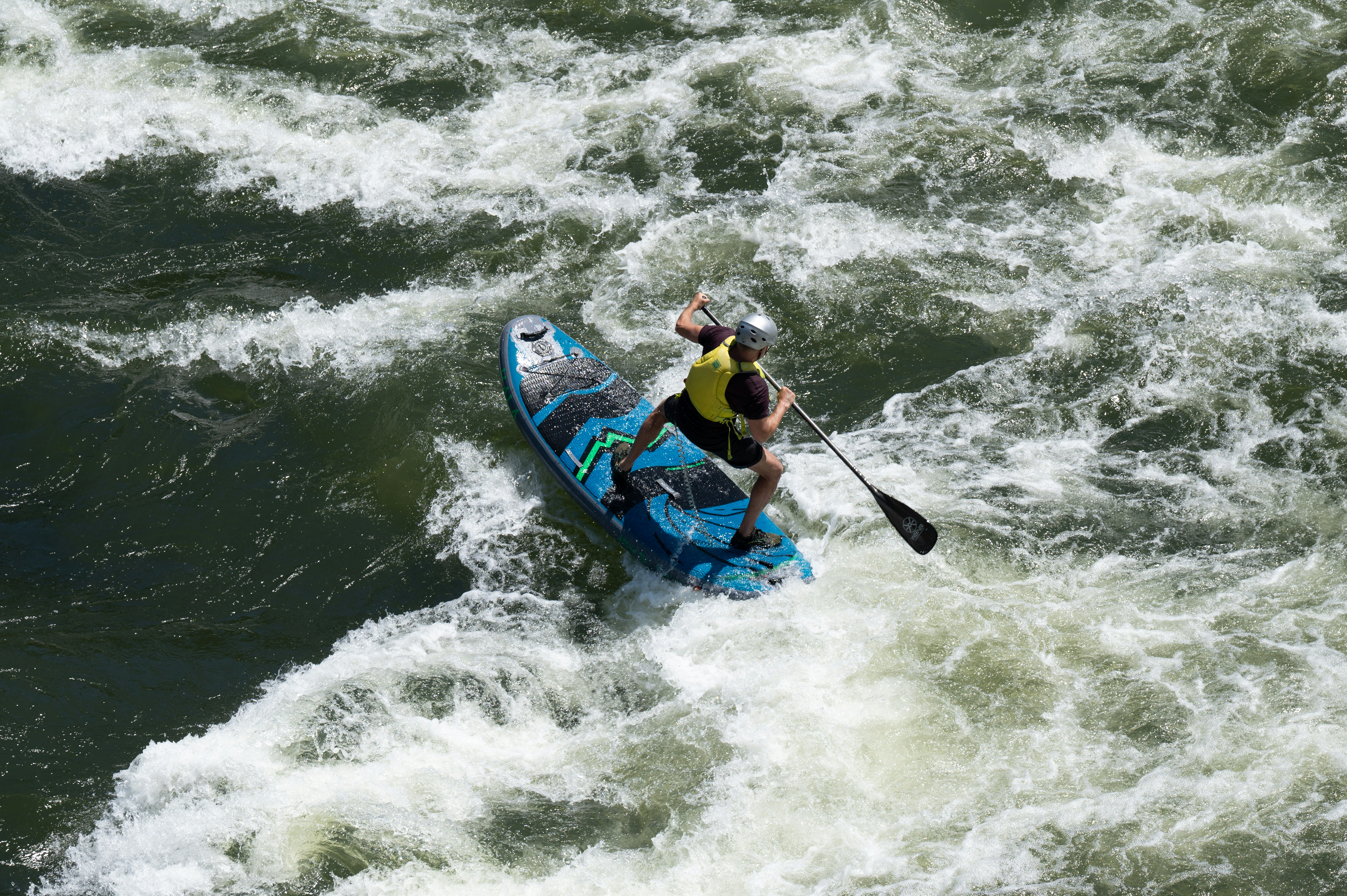 Man paddleboarding through white water rapids in the Potomac River at Great Falls Park, Virginia. | a man riding a surfboard