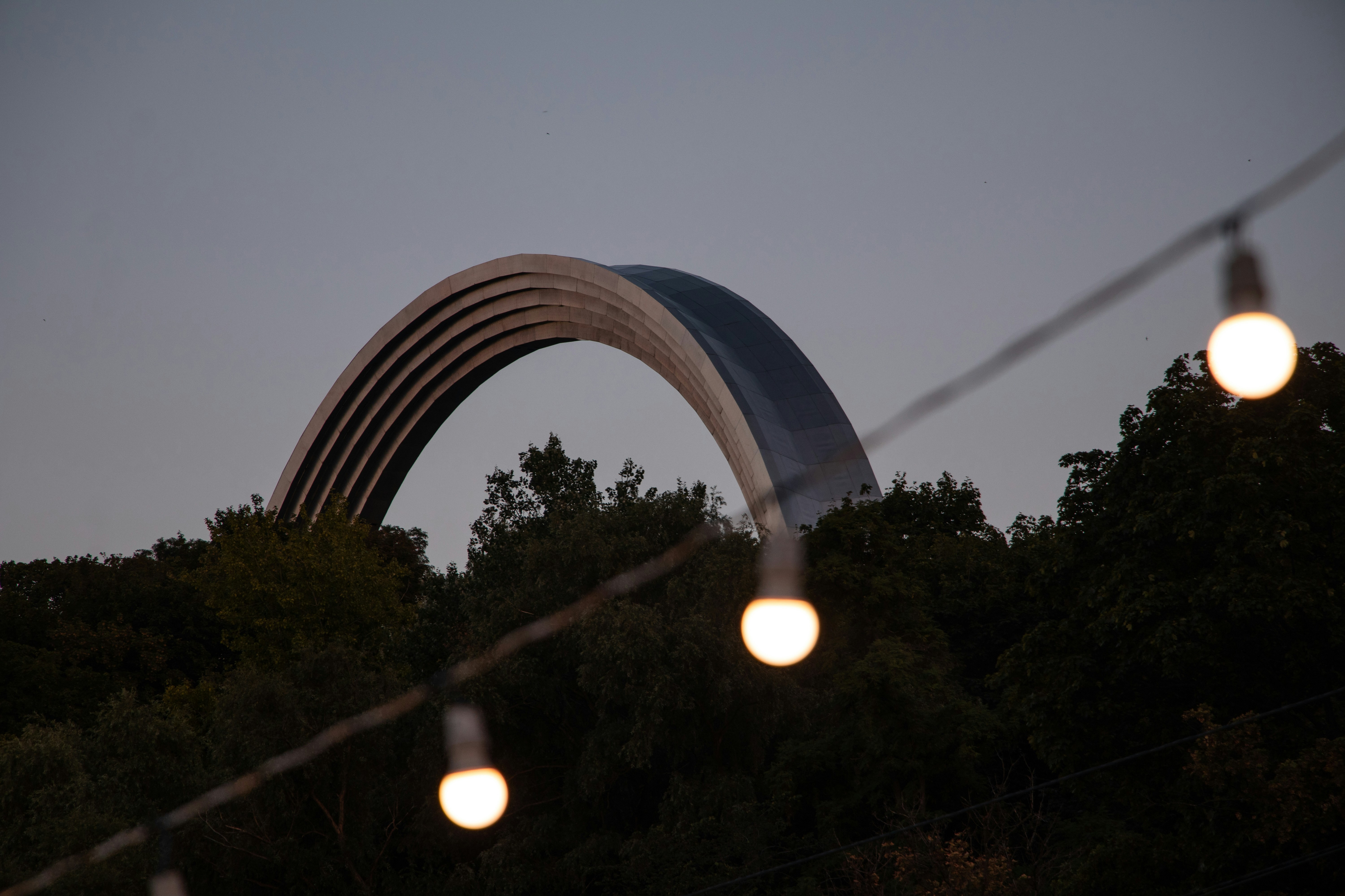 Twilight Arch Emerging Over Trees, Framed by Warm String Lights