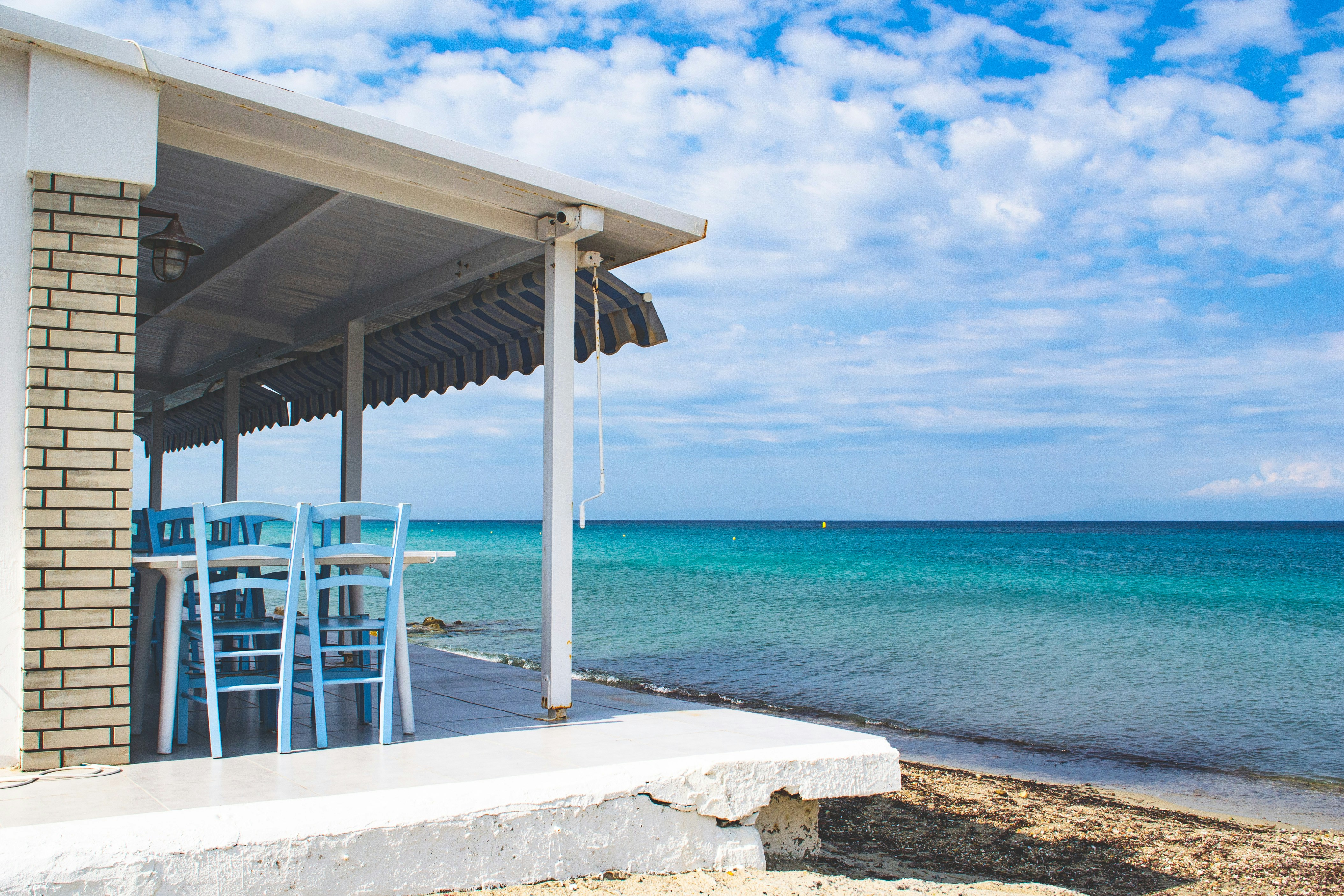 A white building with a white awning and chairs on a beach photo – Free ...