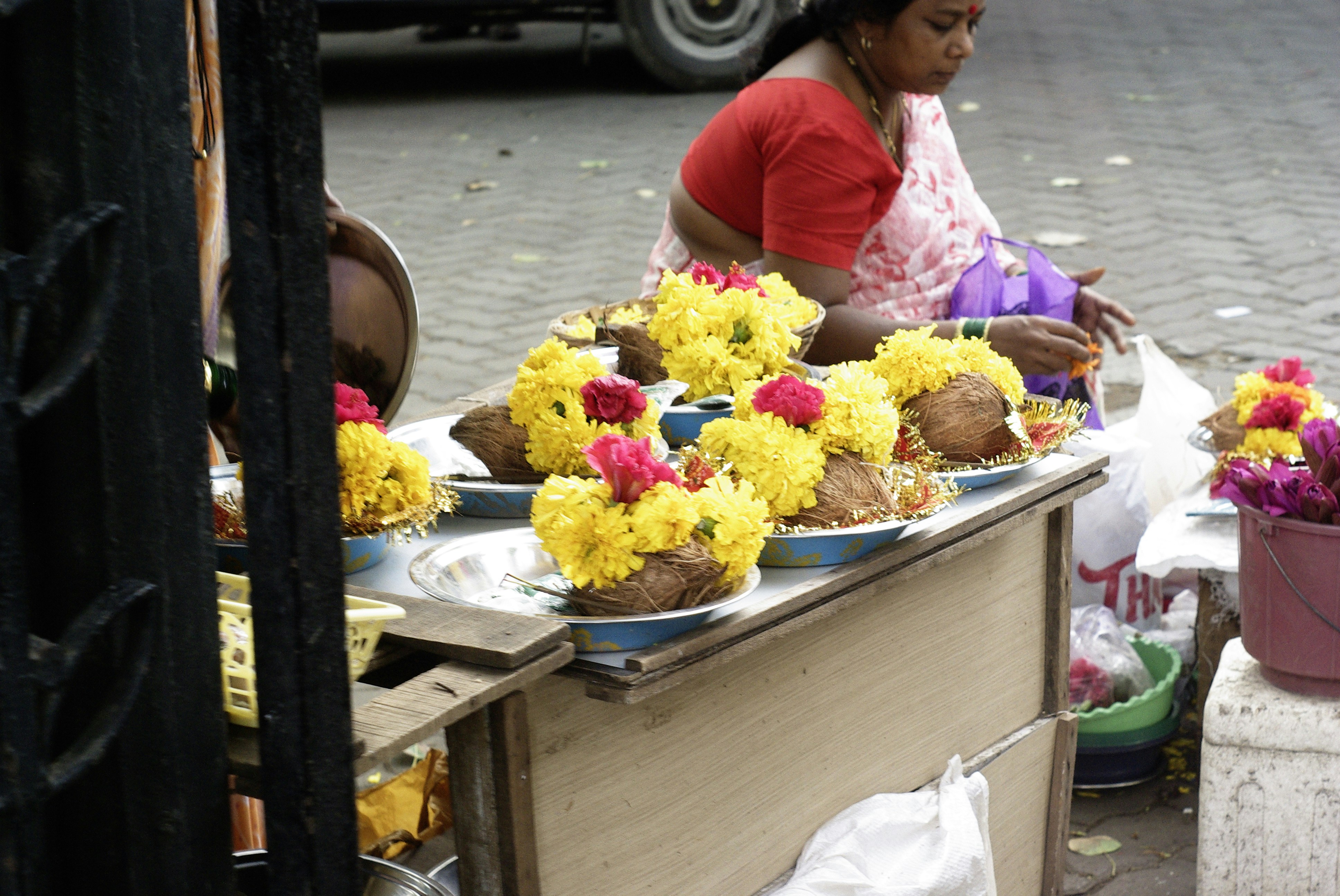 Photograph of a street cart adorned with bright yellow marigolds, with other flowers and market goods visible in the background.