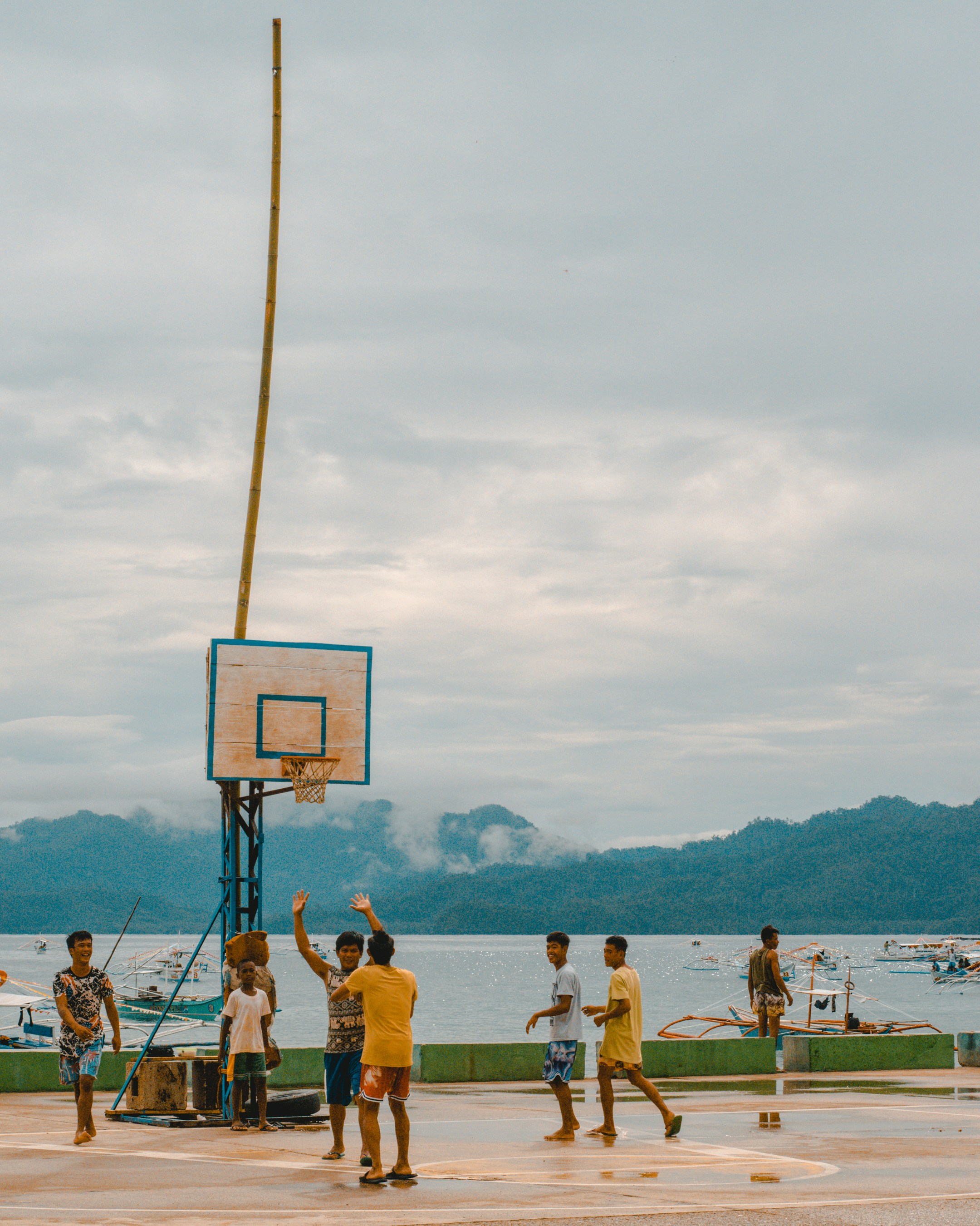 Coastal Court Moment: Kids Play Basketball by a Calm Sea Under Cloudy Skies