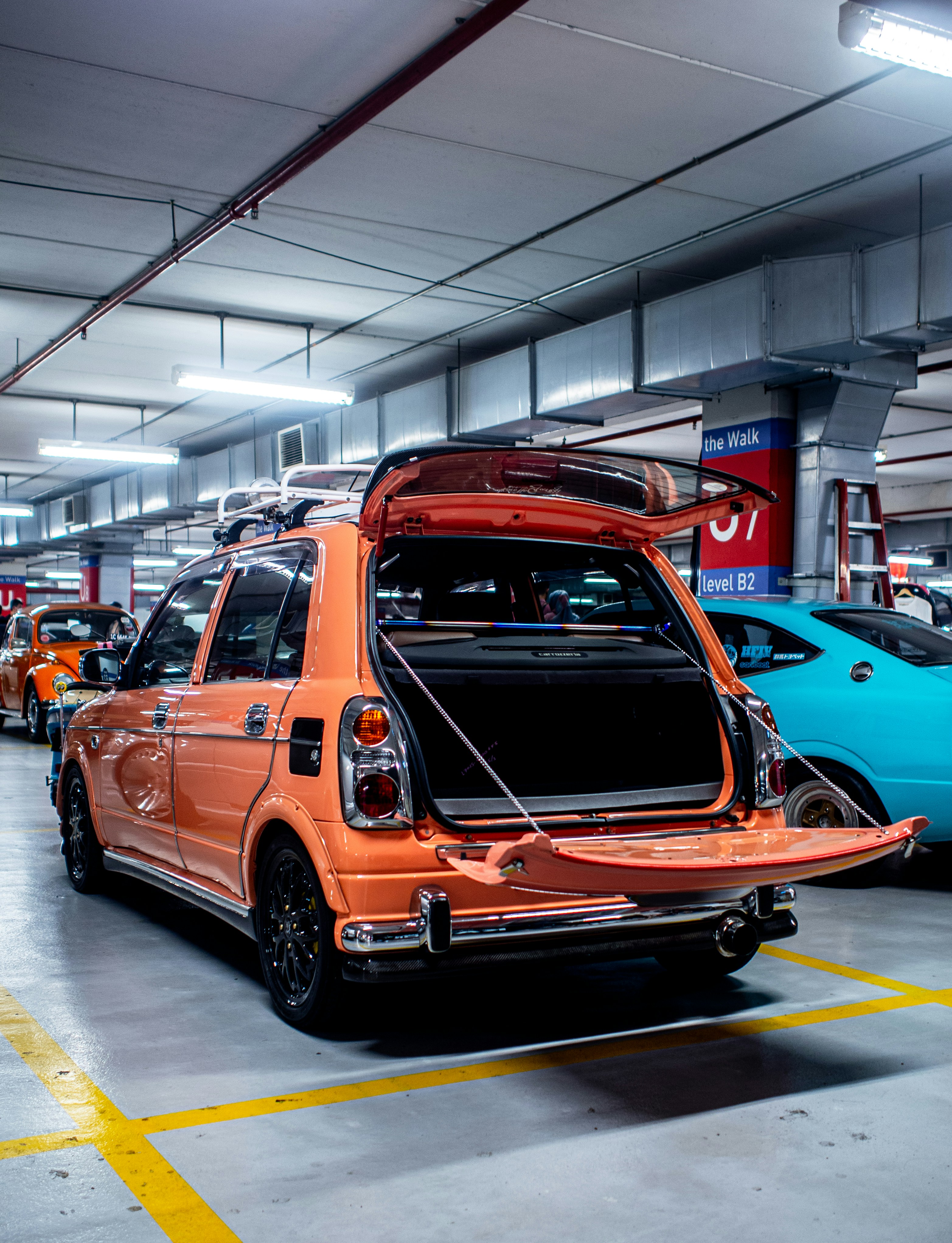Orange vintage hatchback with open rear hatch in a parking garage