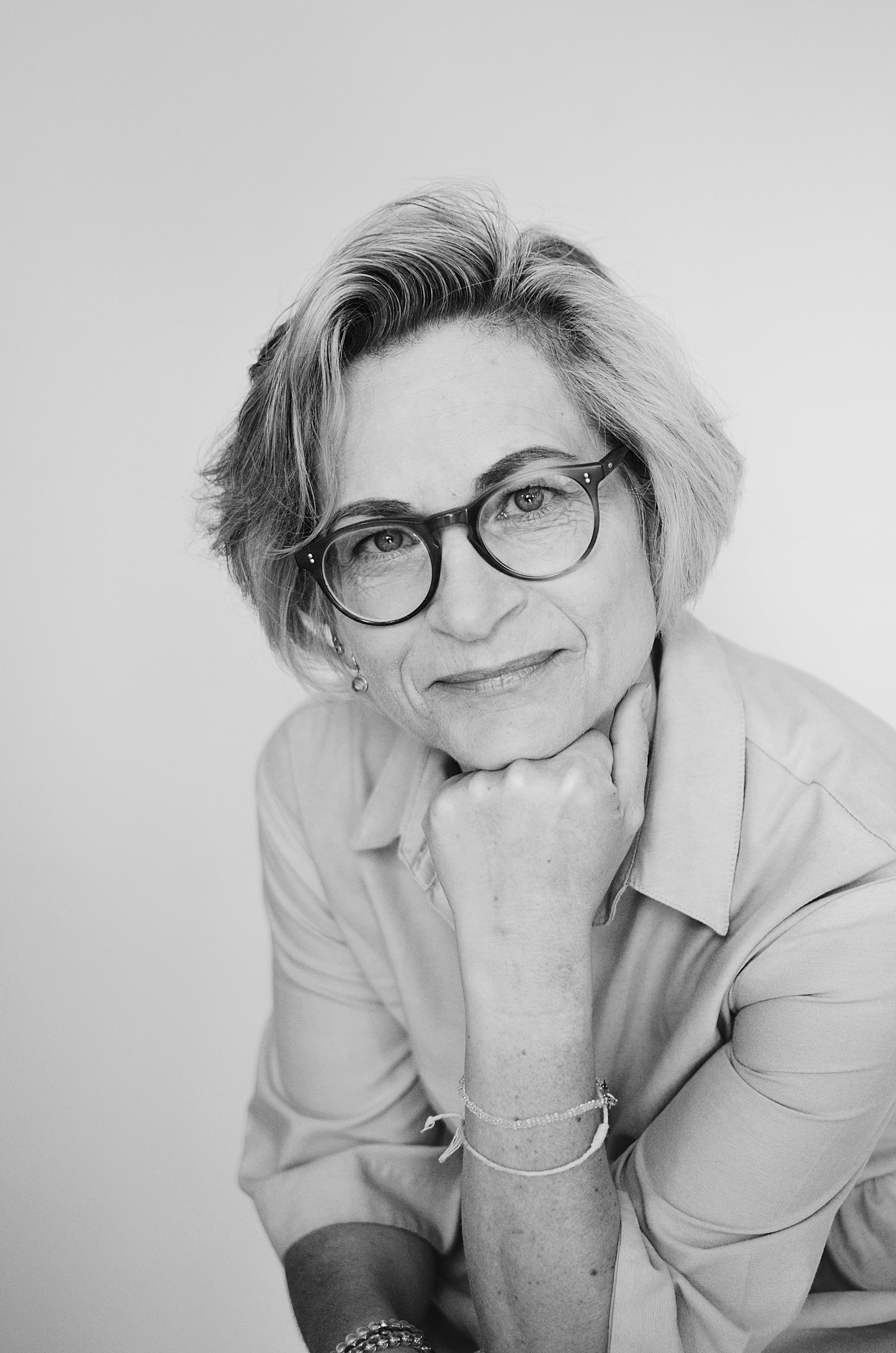 A thoughtful woman resting her chin on her hand, exuding confidence and contemplation against a neutral backdrop.