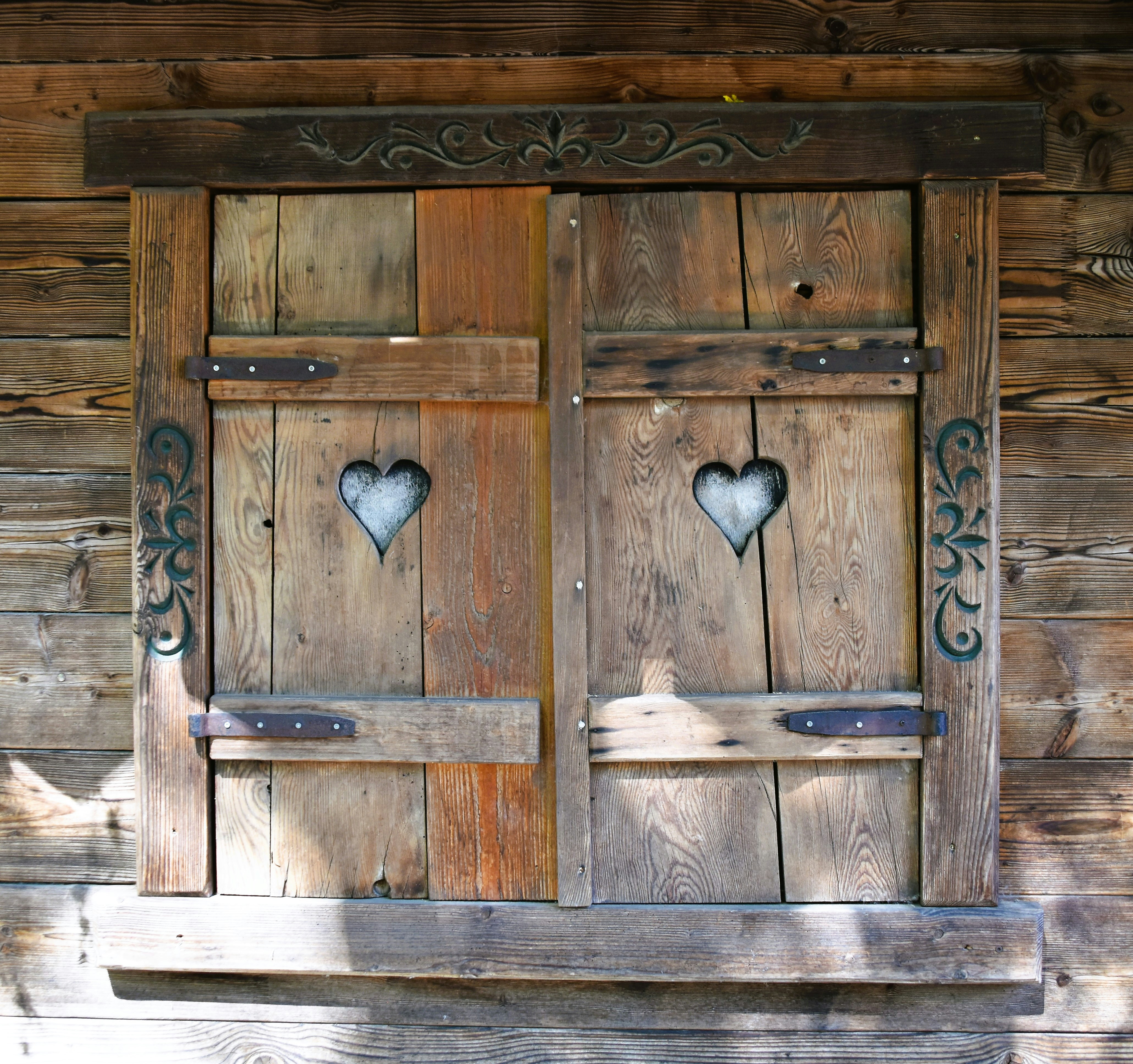 Wooden shutters adorned with heart-shaped cutouts, framed by rustic carvings, evoke a sense of warmth and craftsmanship.