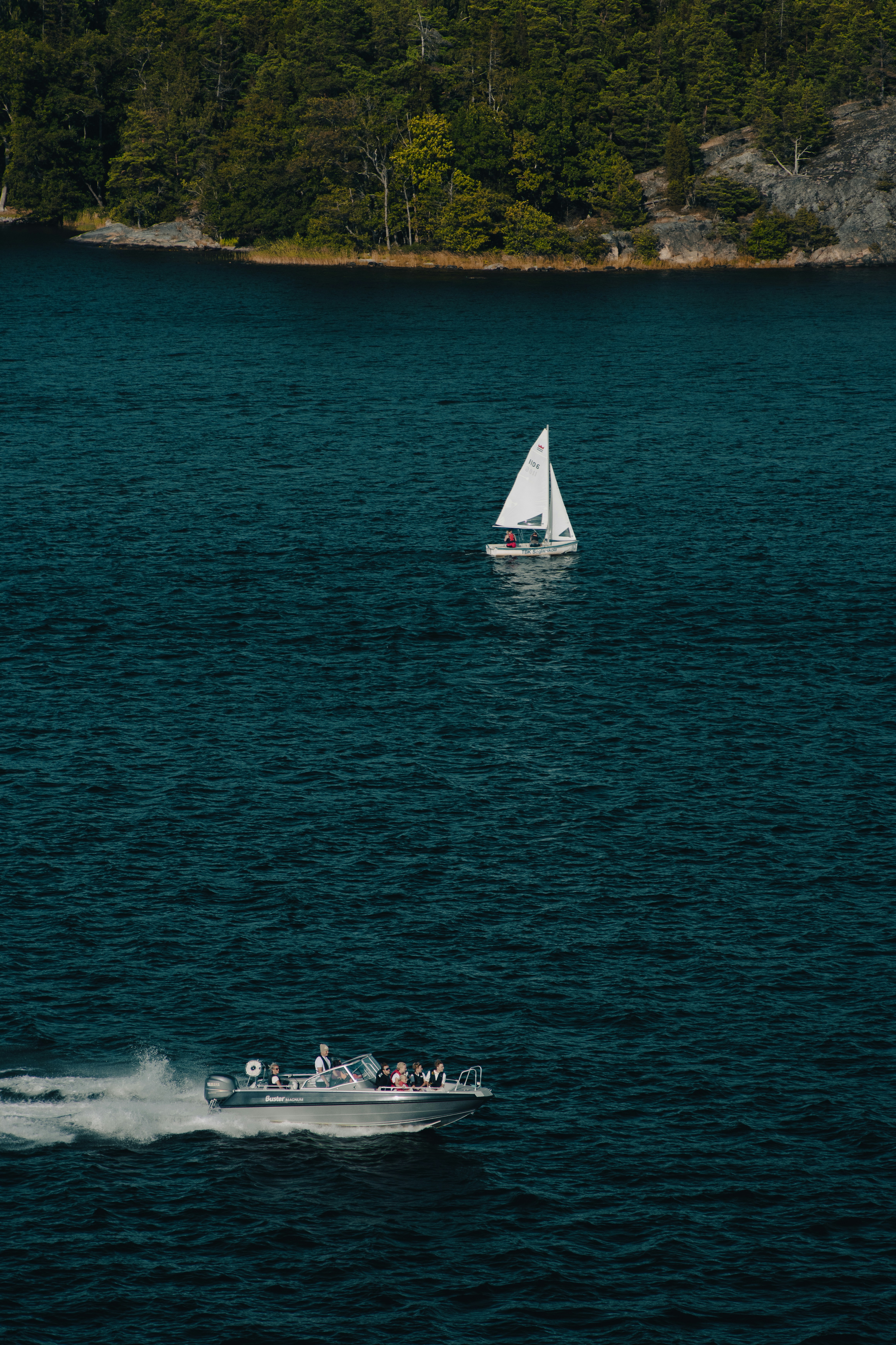 Azure Pursuit: A Speedboat's Wake Heads Toward a Distant Sail on a Deep Blue Lake