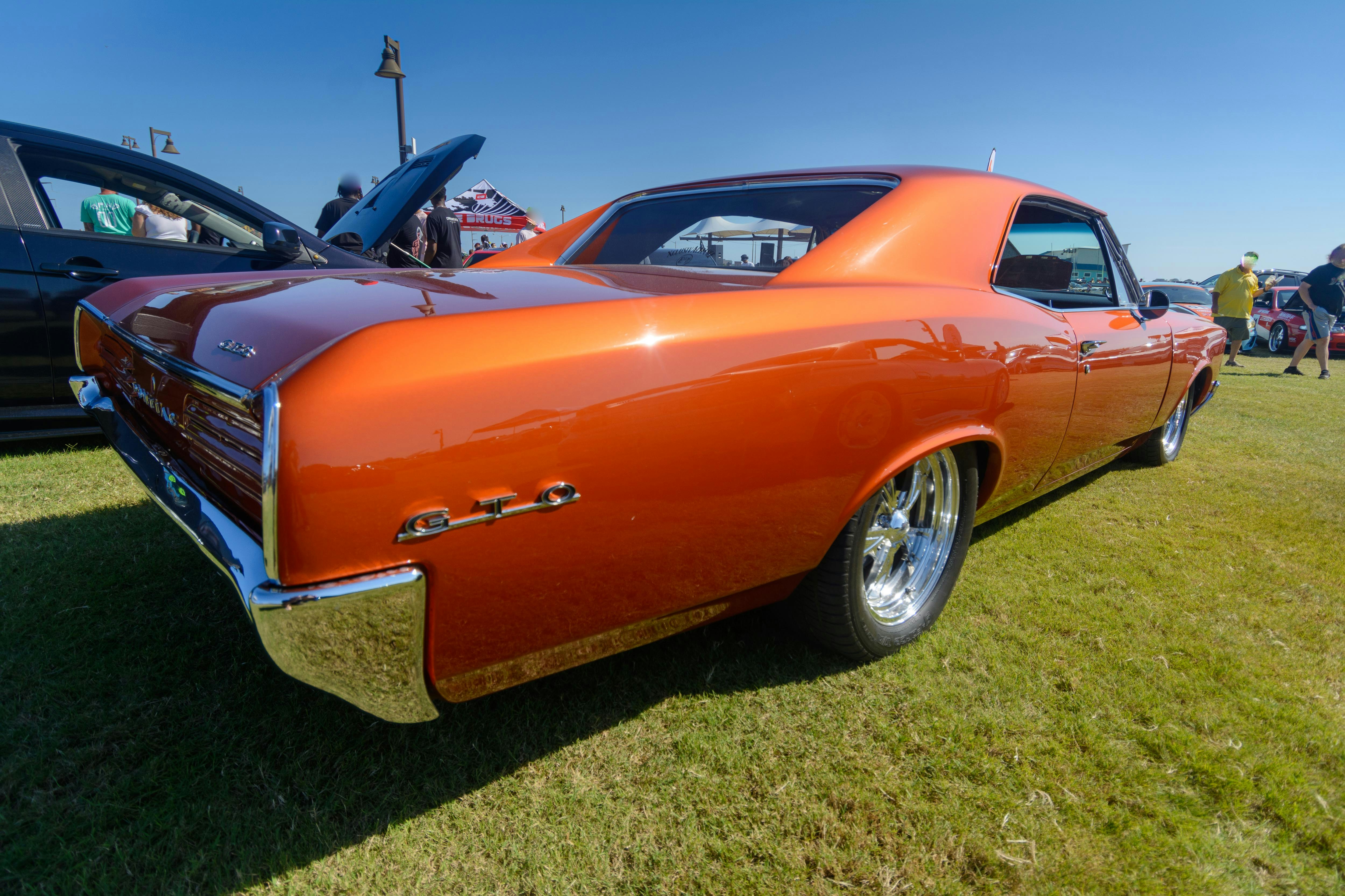 Classic orange muscle car showcasing its sleek lines and chrome detailing at a car show.
