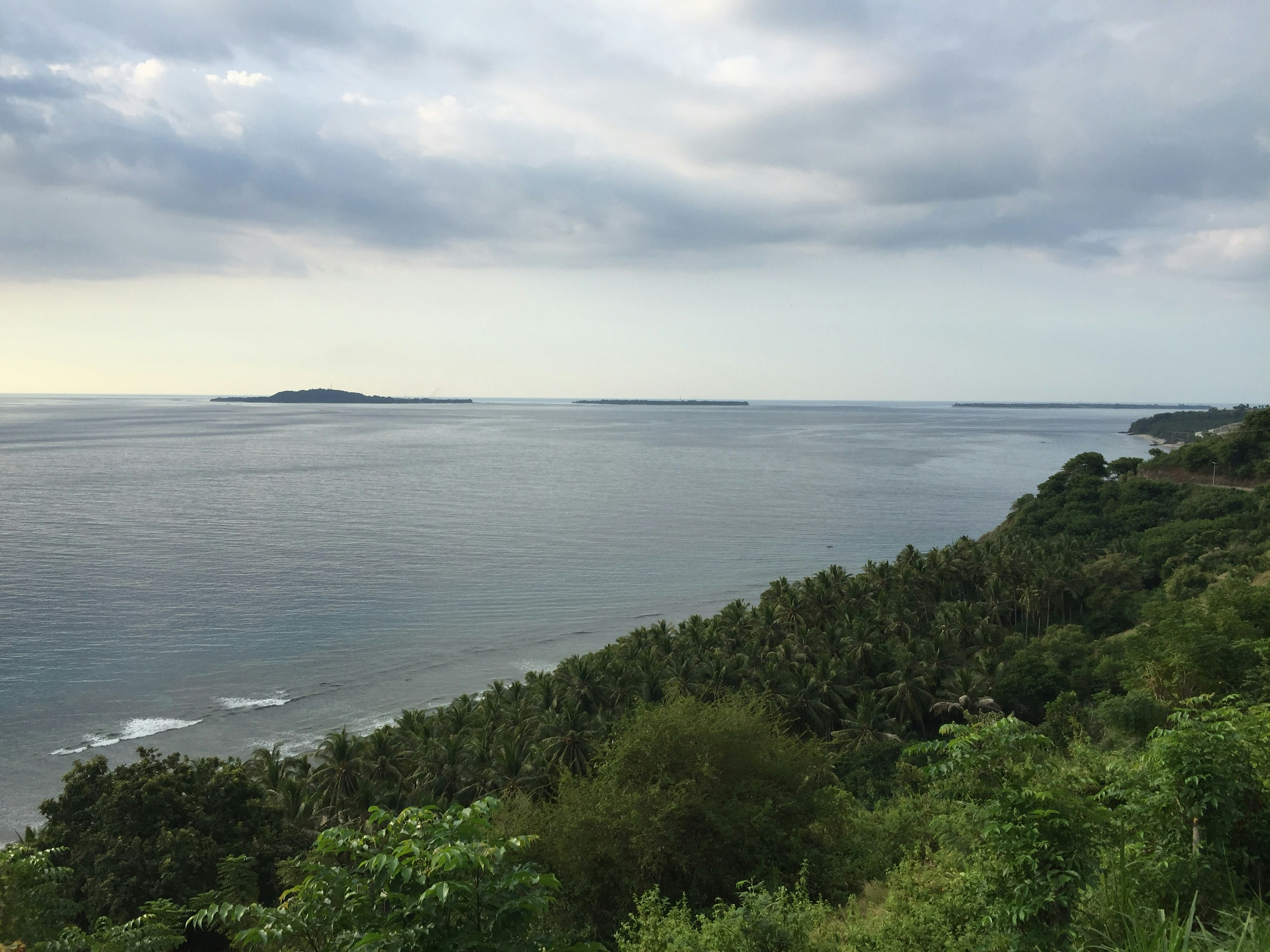 This is at the Malimbu Hill Viewpoint where you can see the 3 Gili Islands. Gili Trawangan is at the left, Gili Meno is at the center, and Gili Air is on the right, closer to the mainland. | a body of water with trees on the side