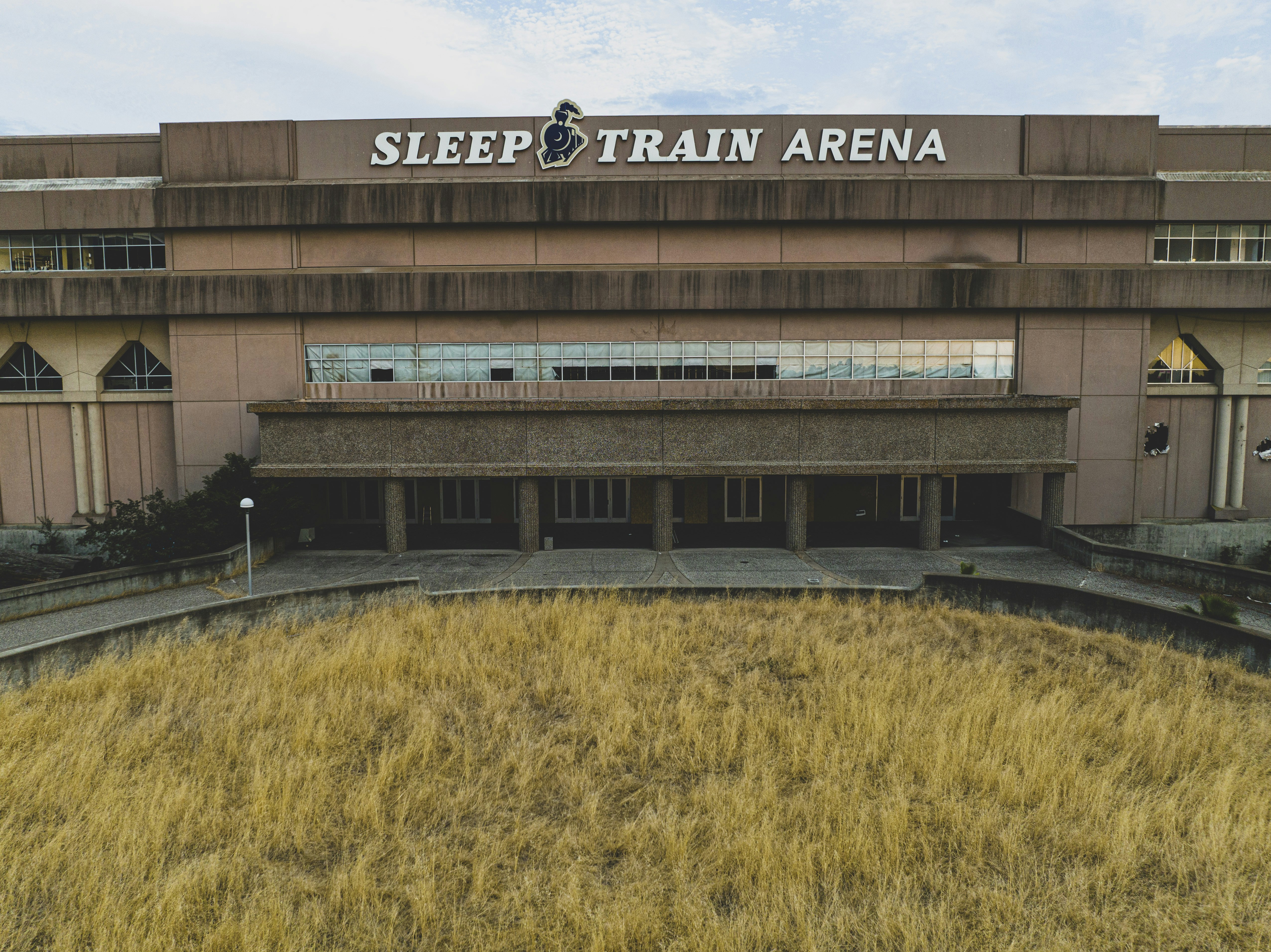 Stoic Gateway: Sleep Train Arena framed by a windswept field of yellow grass
