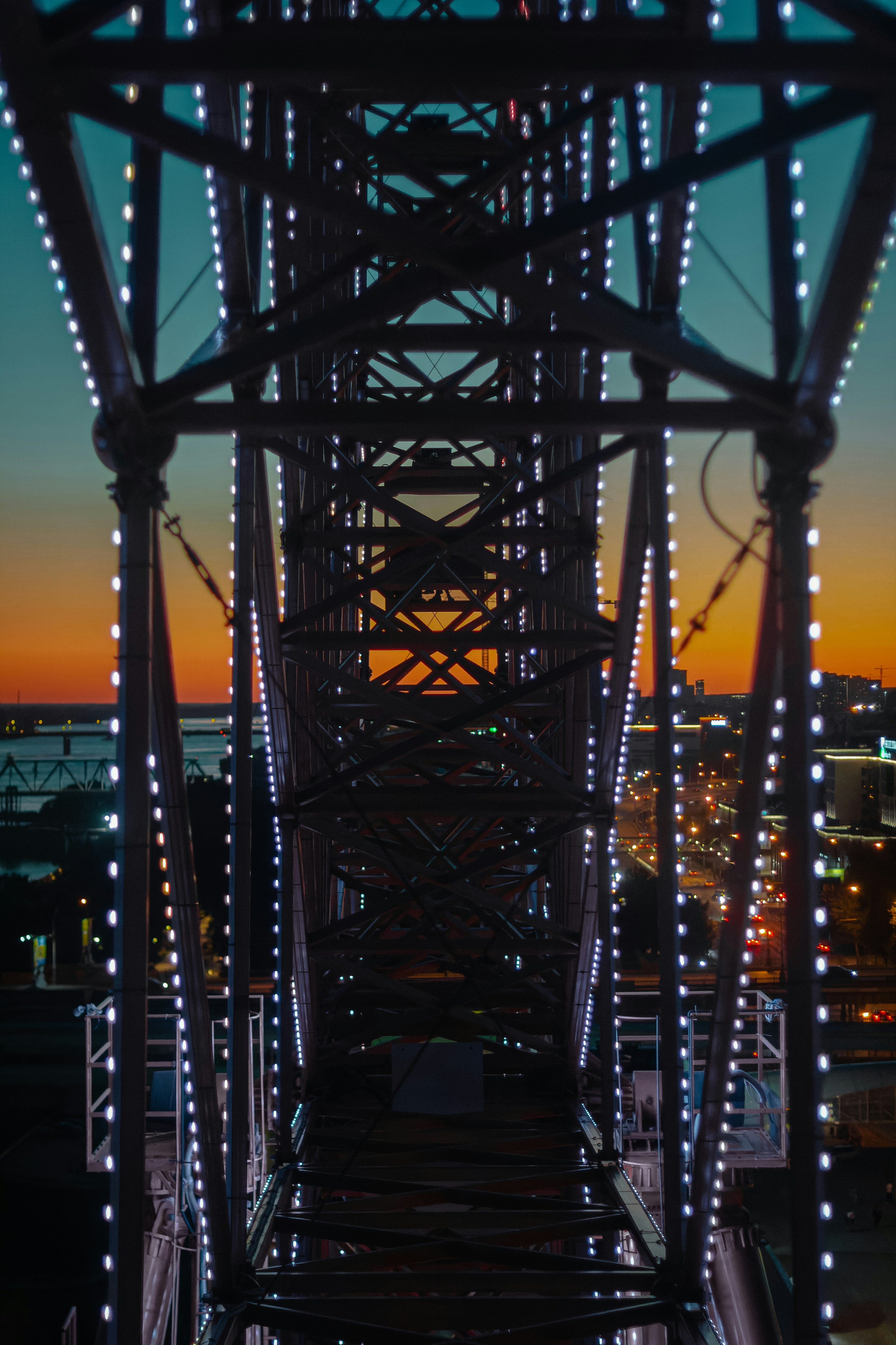 Illuminated ferris wheel structure with a vibrant sunset backdrop, showcasing city lights below.