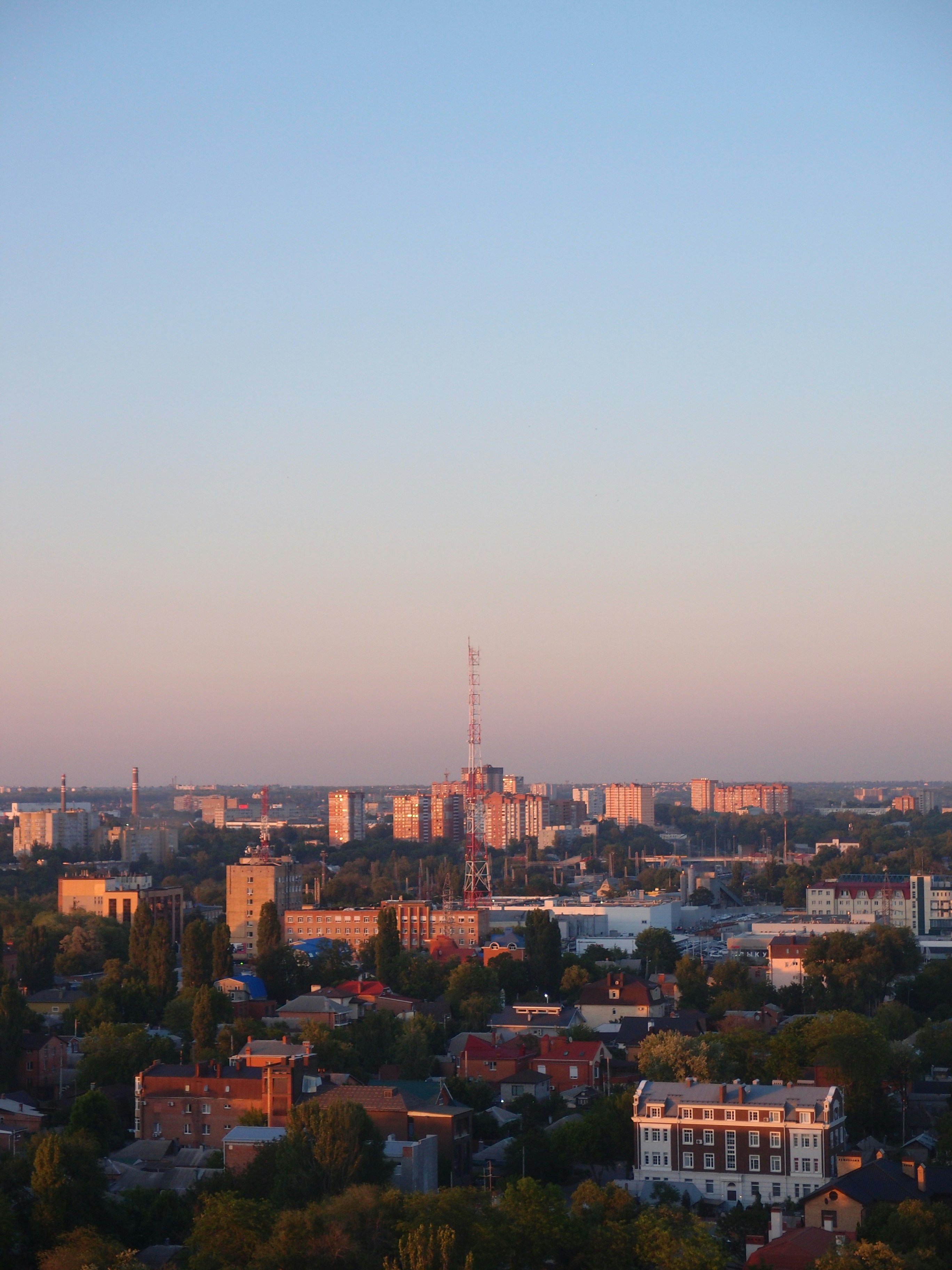 A panoramic view of a city skyline bathed in the warm hues of twilight, showcasing a mix of residential buildings and communication towers.