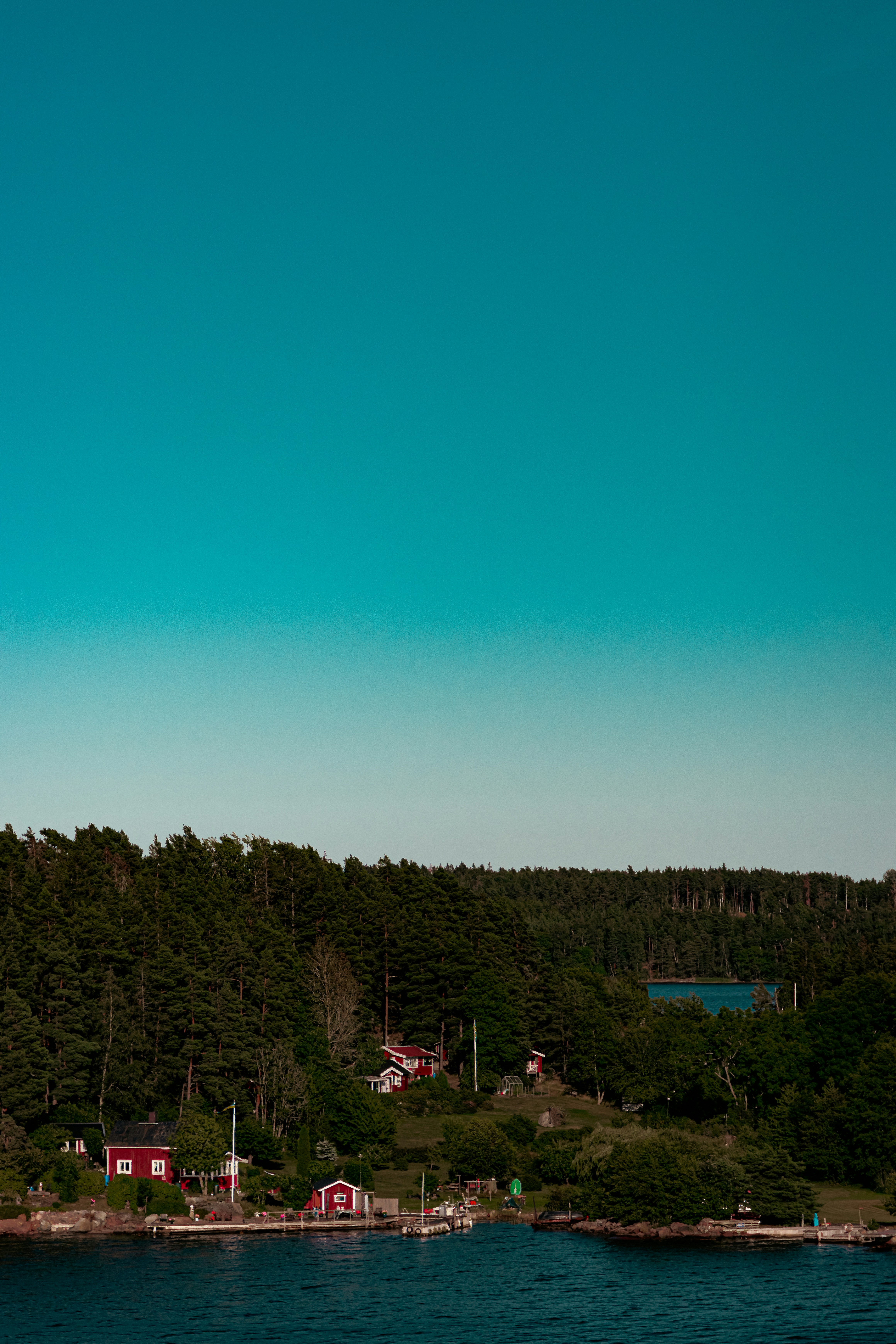 Red Dwellings at the Shoreline Under a Teal Sky