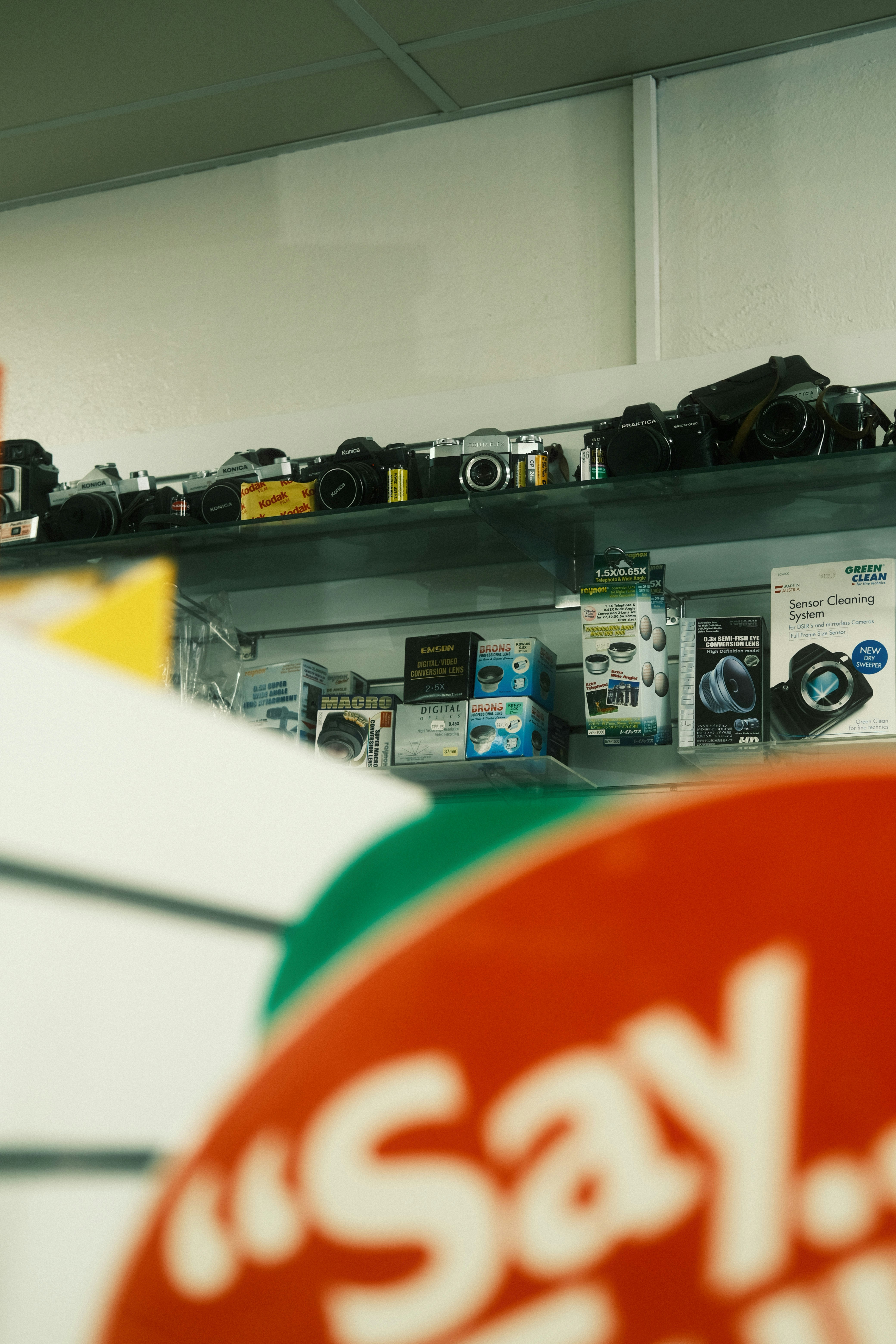 Cameras in Focus: A Glass-Shelf Row Beneath a Blurred Sale Sign