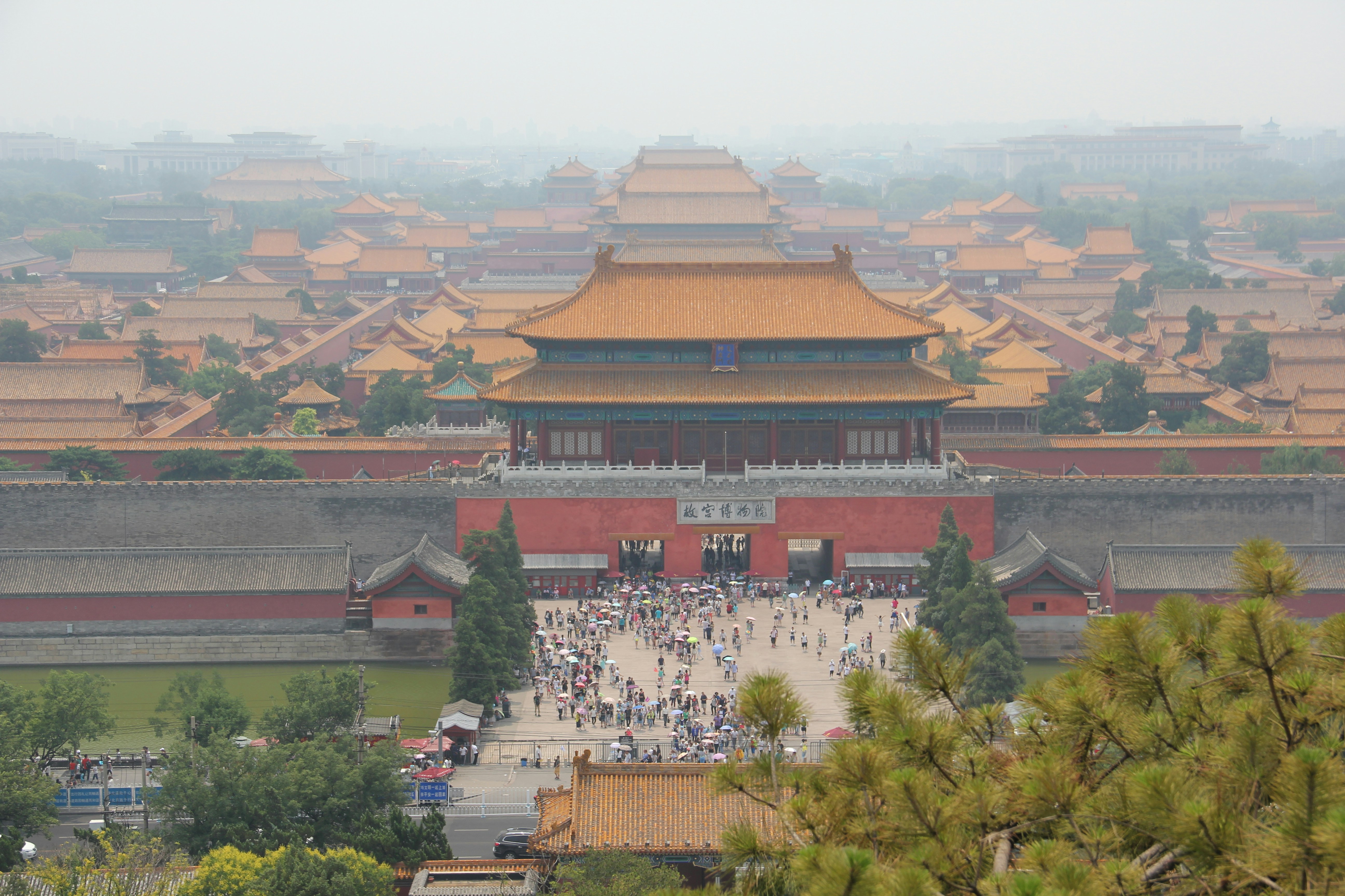 Overlook of the Forbidden City with its iconic yellow roofs and bustling crowds, shrouded in light mist.