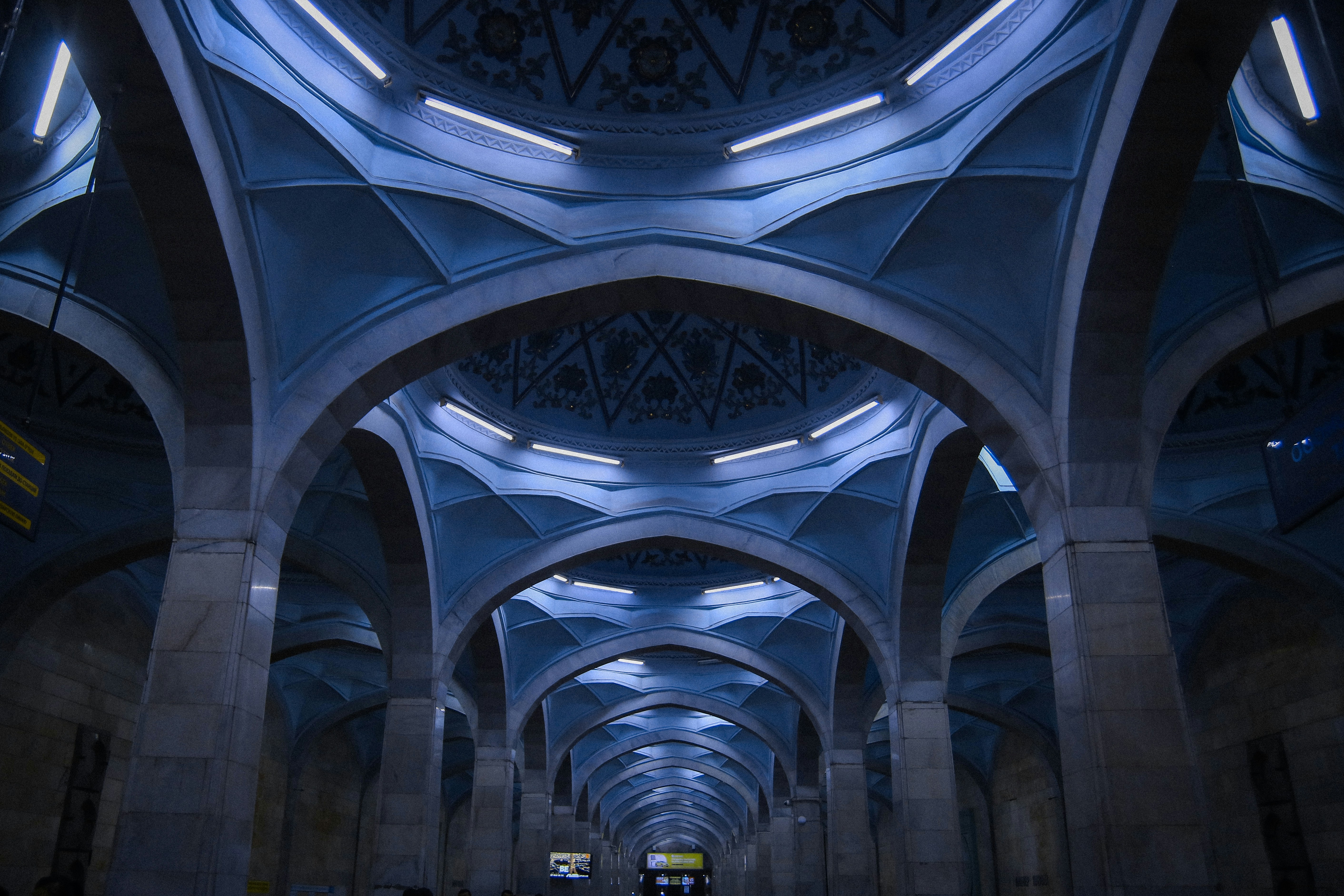 Modern architectural ceiling with illuminated blue arches and geometric patterns.