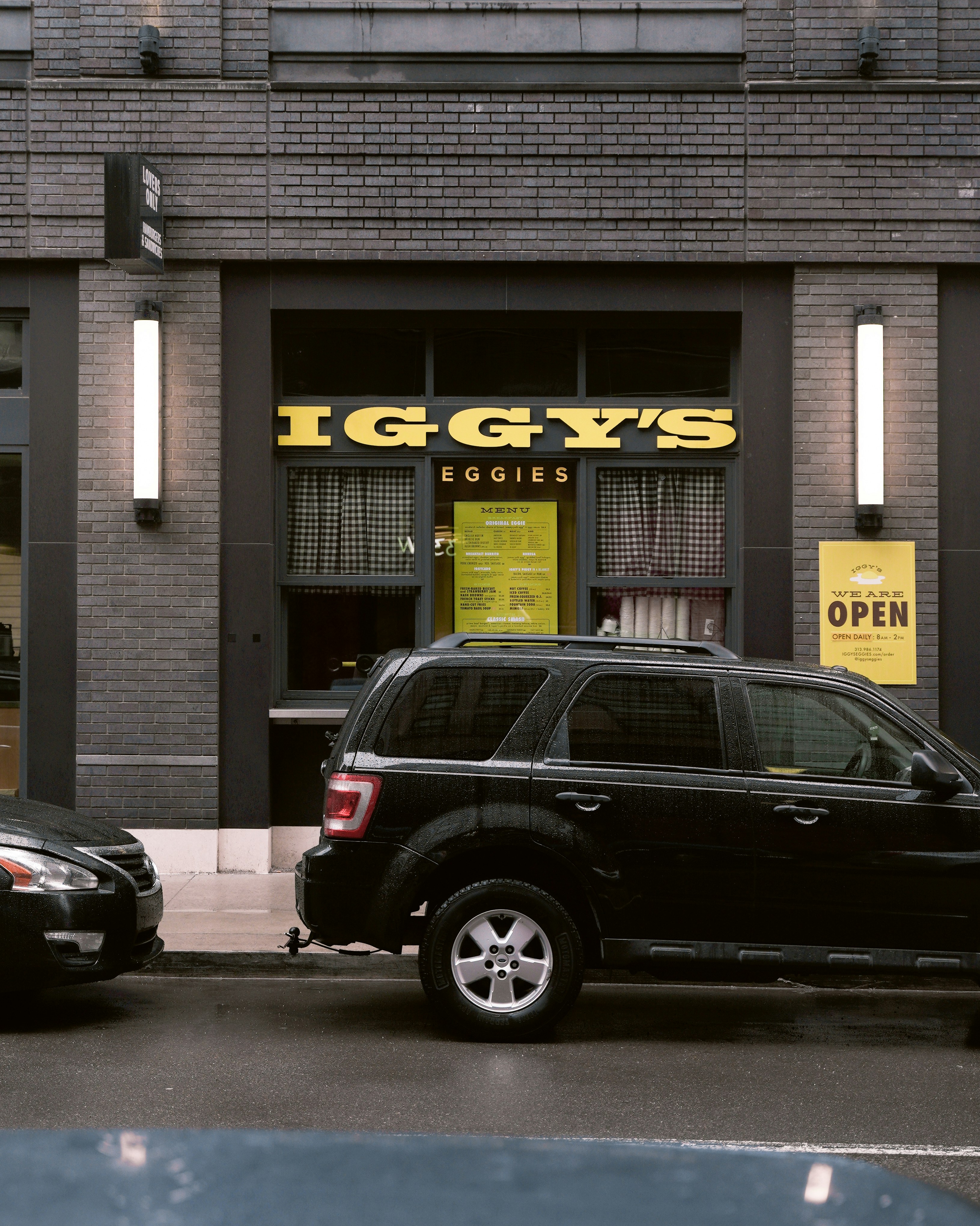 Urban storefront and parked SUV under a brick façade