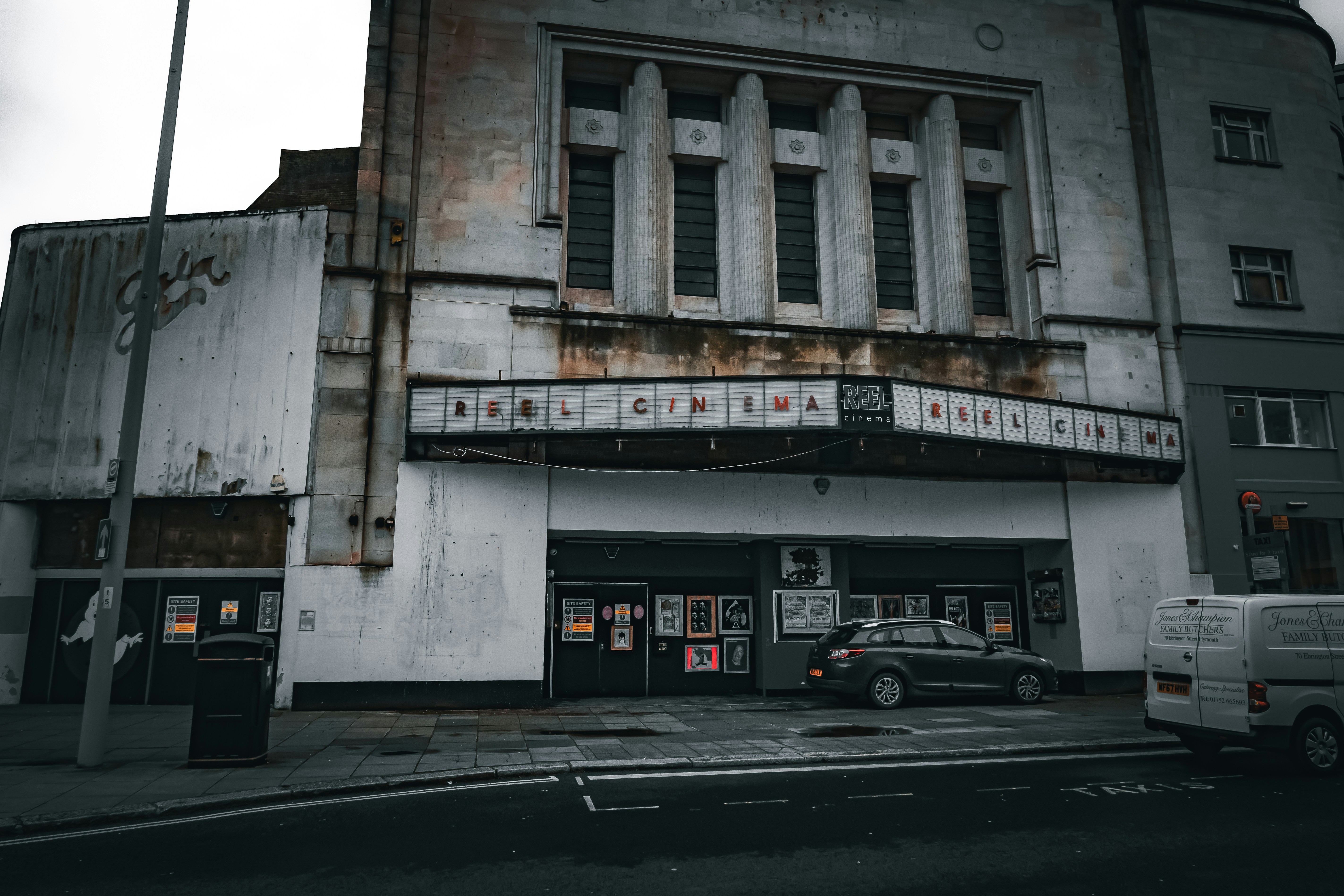 Historic cinema with vintage marquee and weathered facade, featuring tall columns and parked vehicles in front.