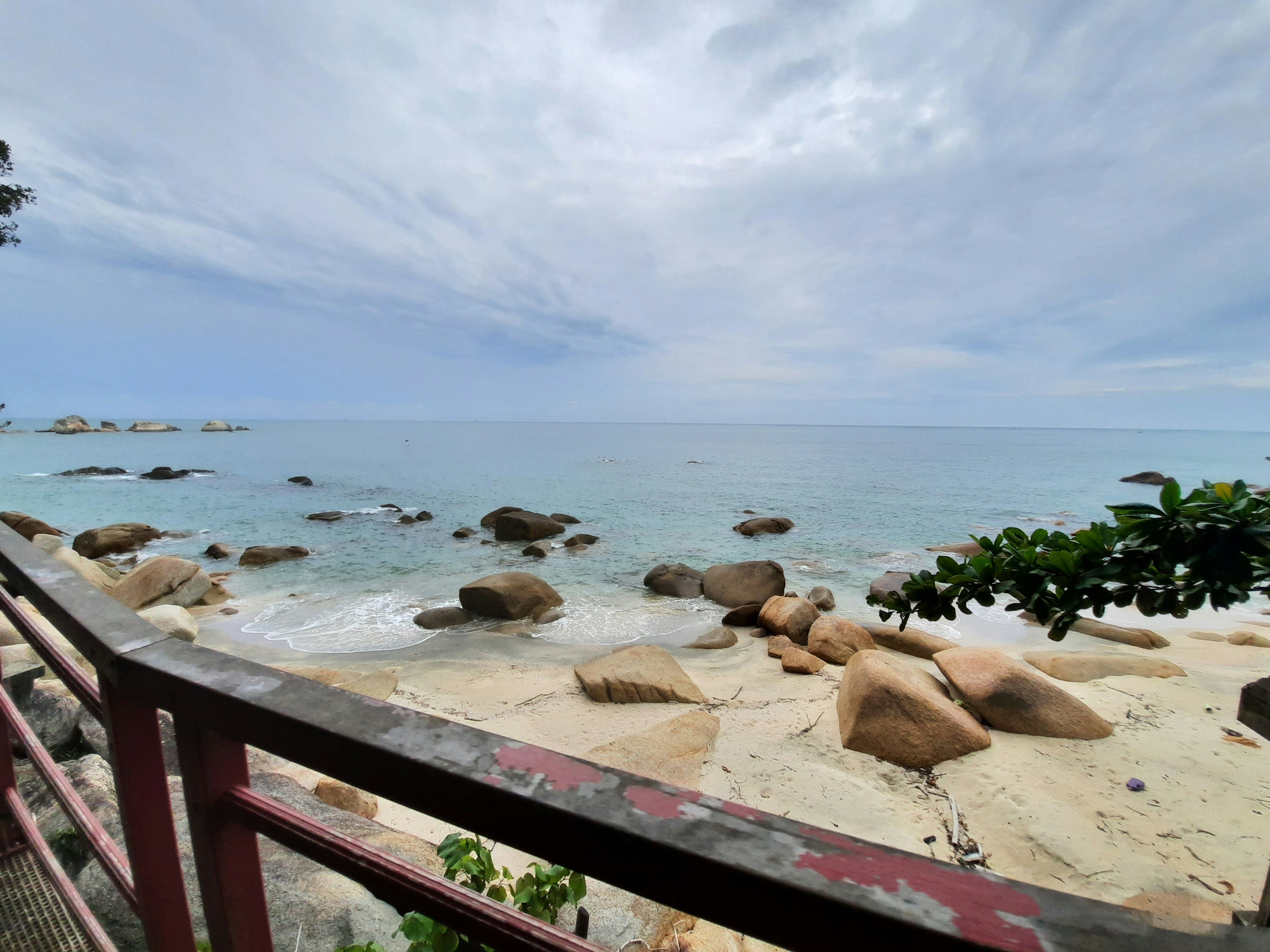 Weathered Rail Framing a Boulder Beach Beneath a Calm Sea Sky