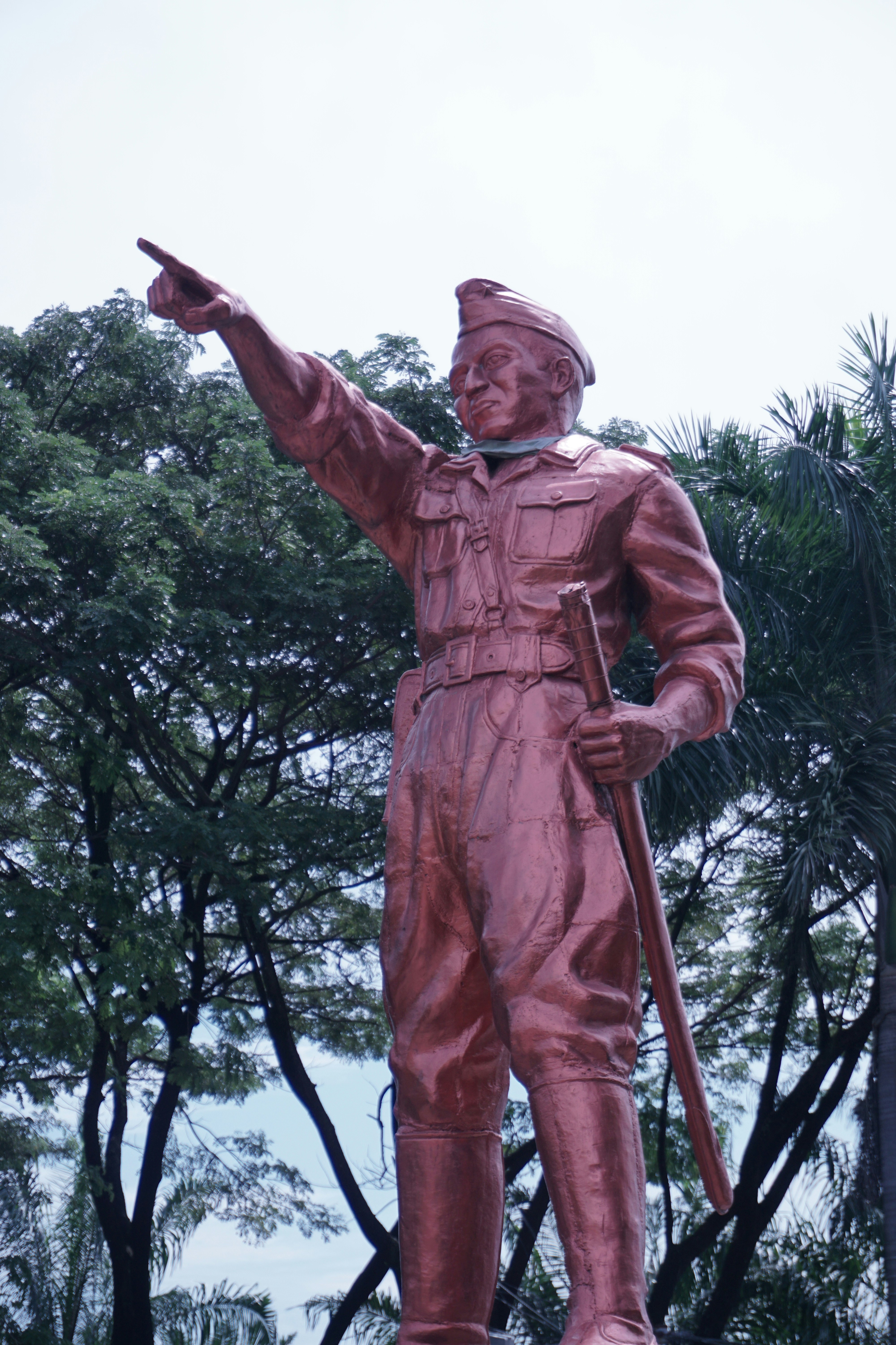 Bronze statue of a military figure pointing towards the horizon, surrounded by lush greenery.
