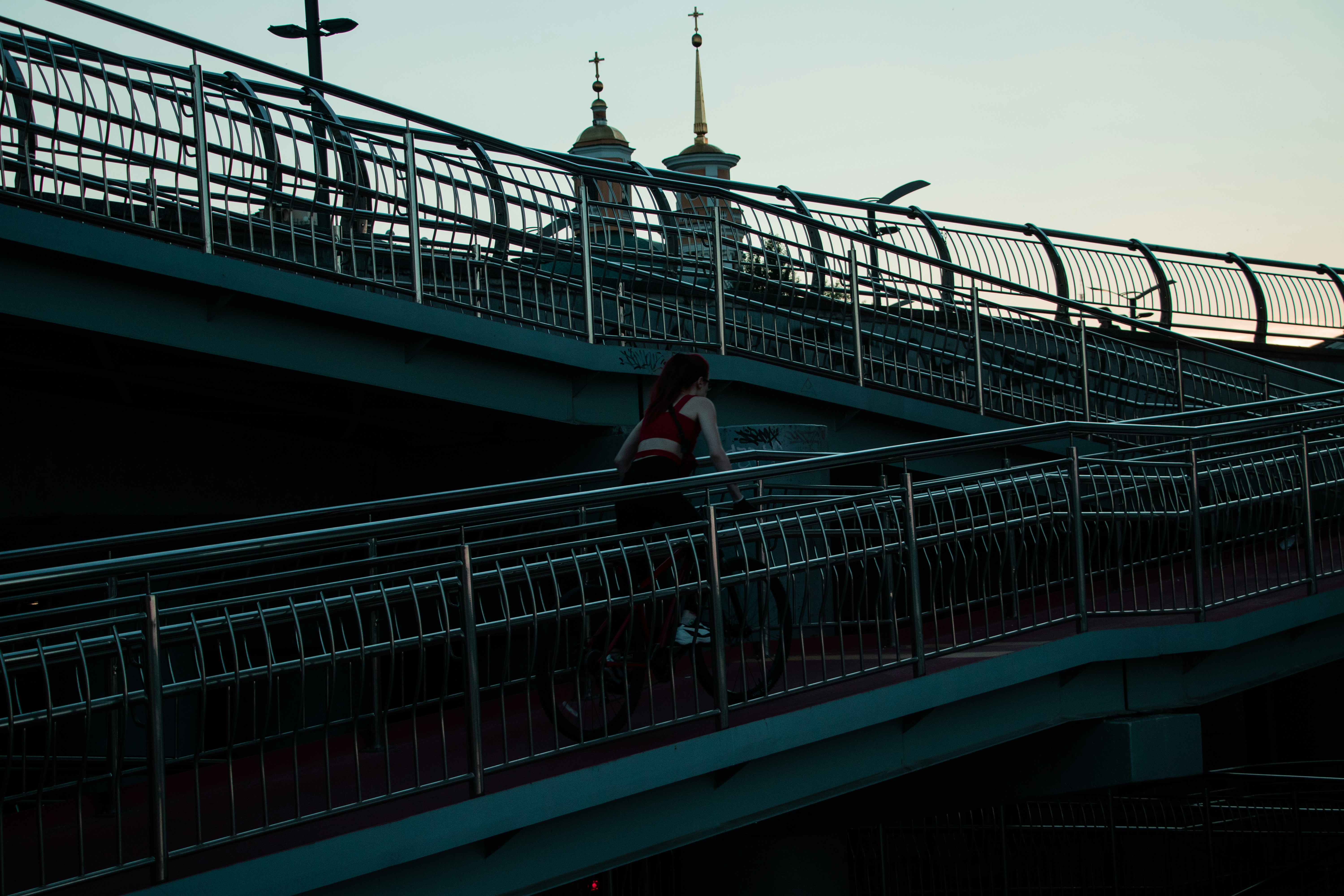 Twilight Ascent: A lone figure threads the steel spine of a city pedestrian bridge