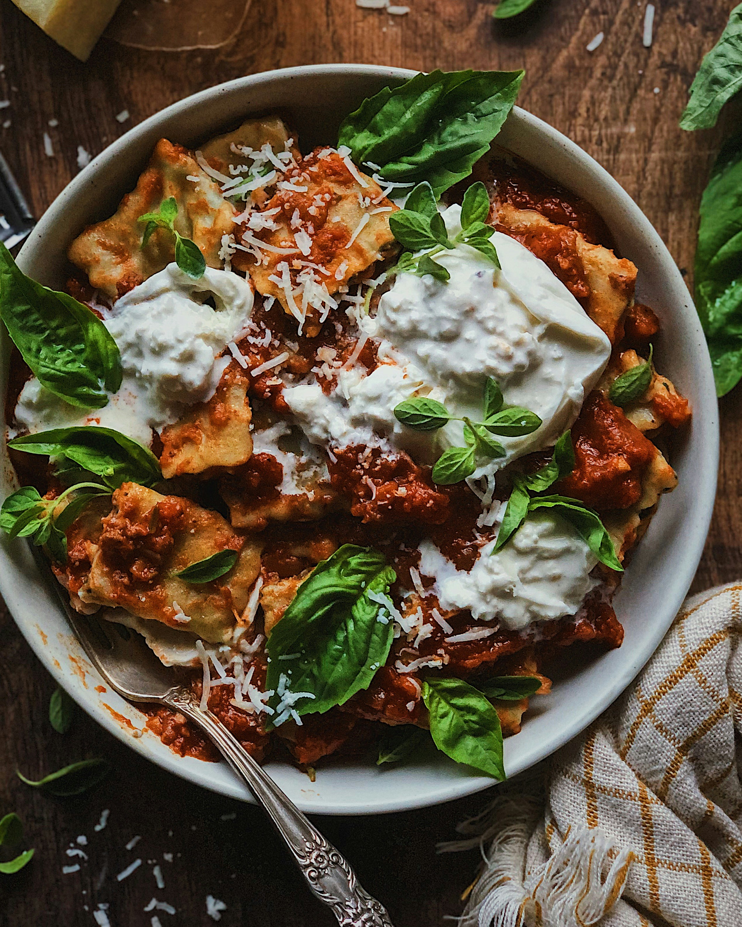 A bowl of ravioli topped with rich tomato sauce, fresh basil, and creamy ricotta, garnished with grated cheese.