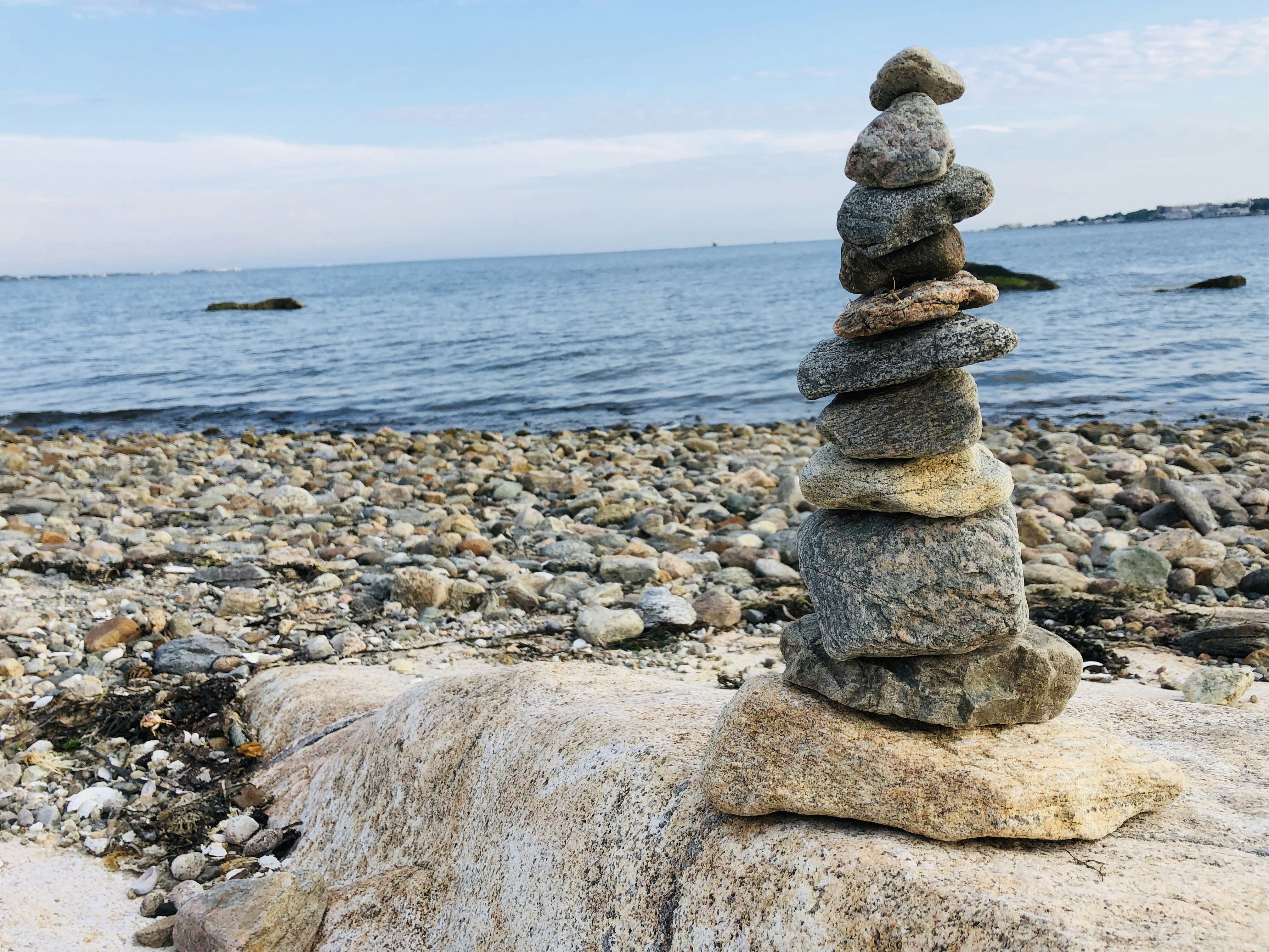 Stone cairn stacked on a rocky beach with the ocean in the background.