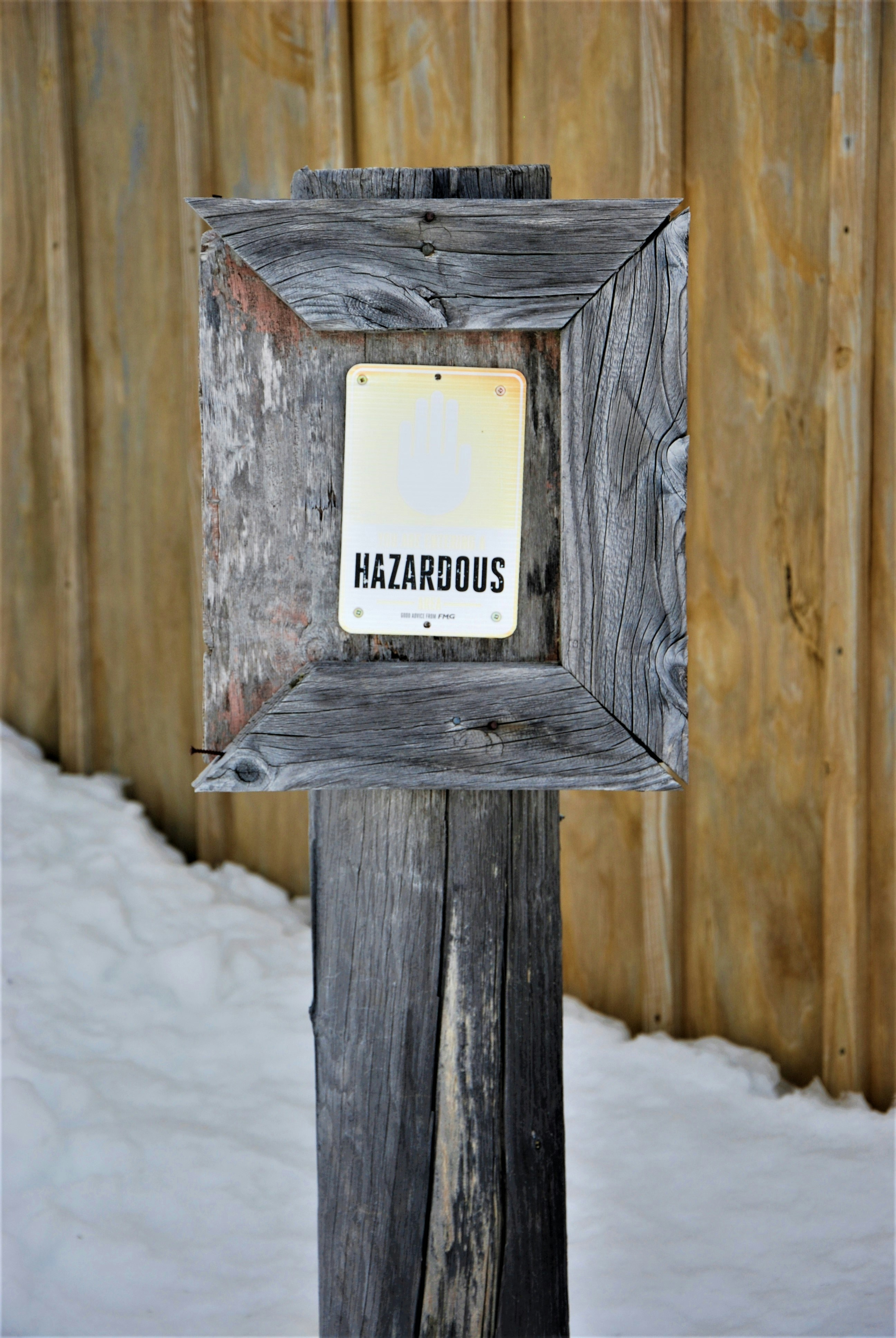 Weathered wooden sign displaying a 'HAZARDOUS' warning, set against a backdrop of snow and rustic wood.