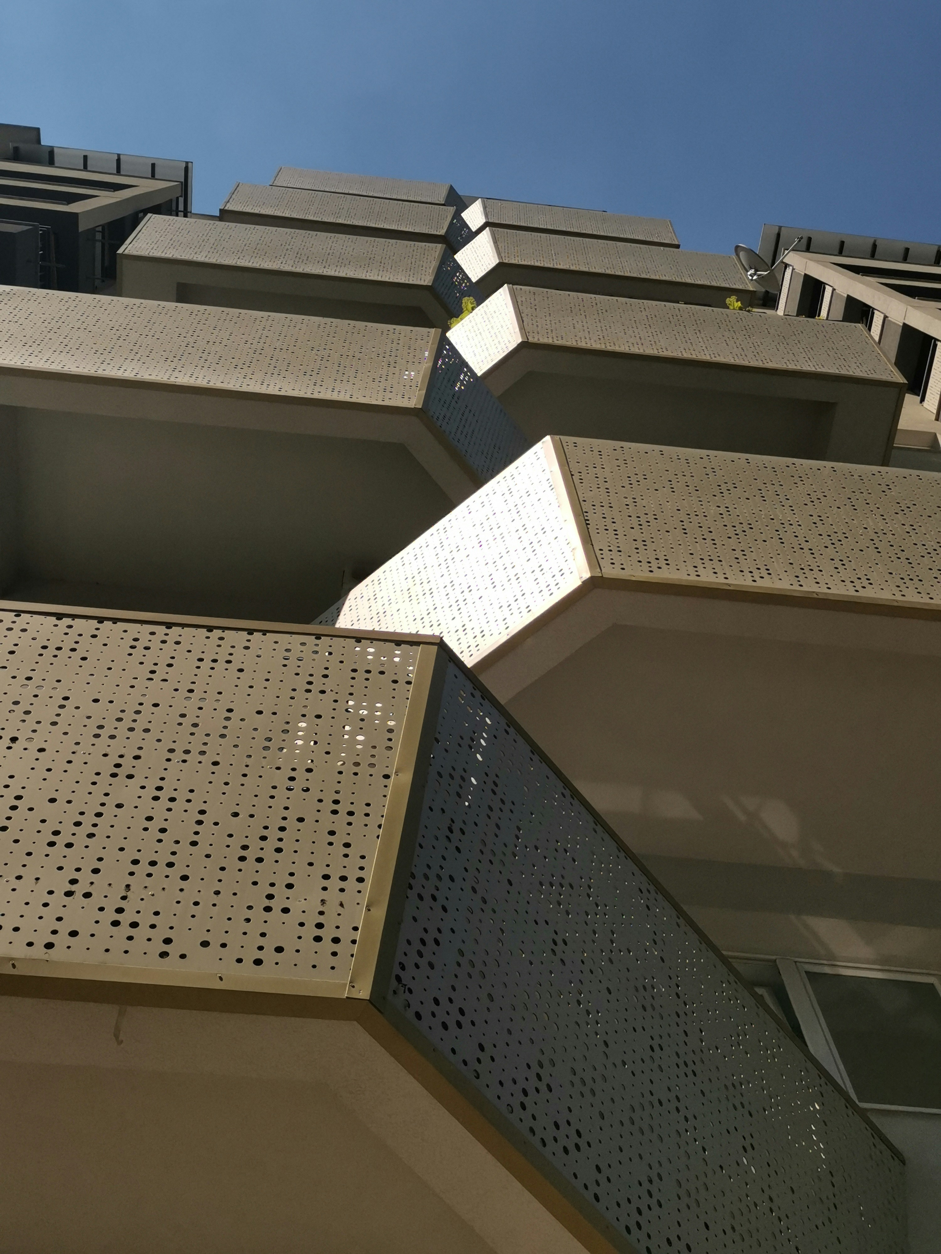 Modern building facade showcasing intricate balcony patterns under a clear blue sky.