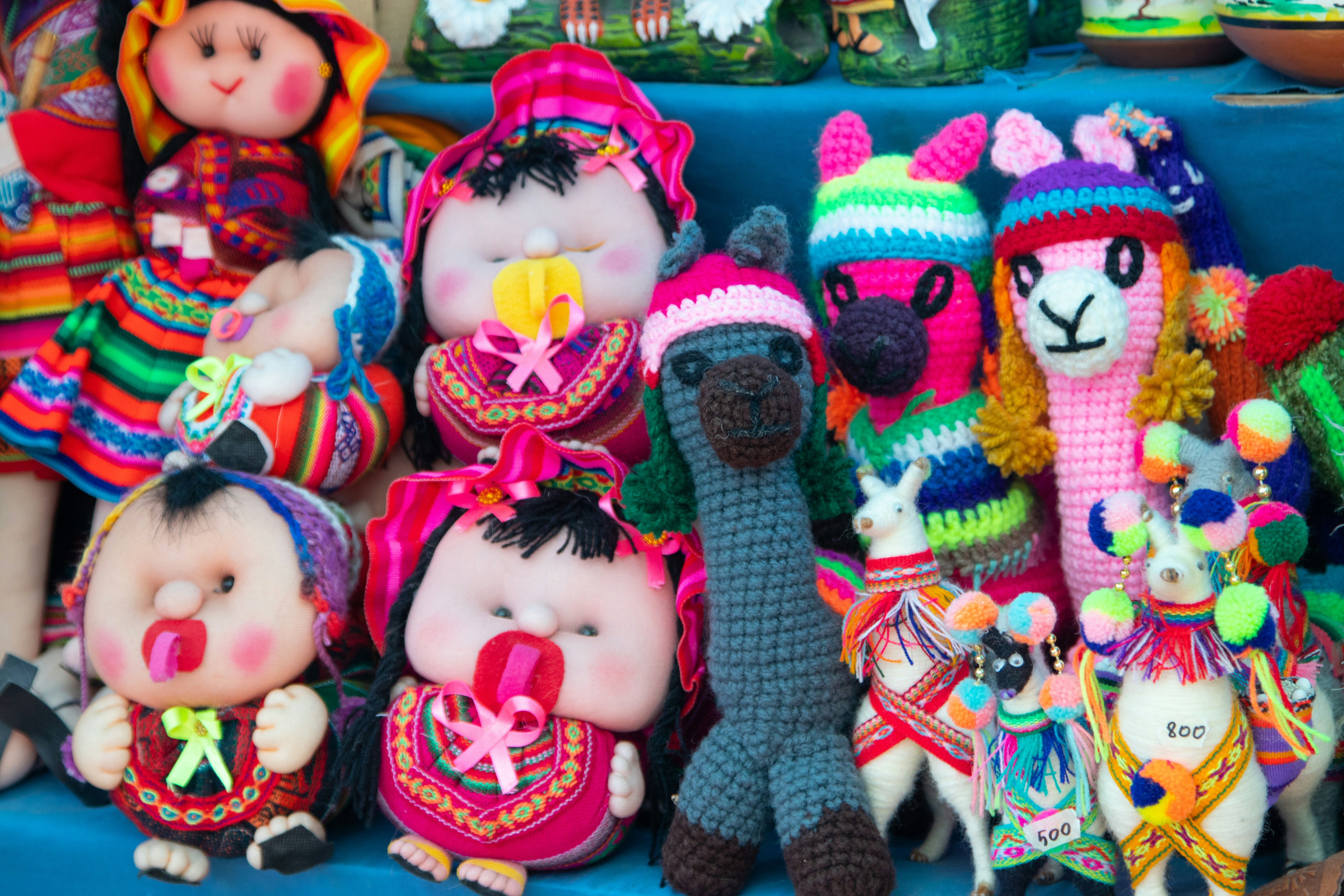 Center Stage: The Gray Crochet Llama Among a Rainbow of Plush Market Dolls