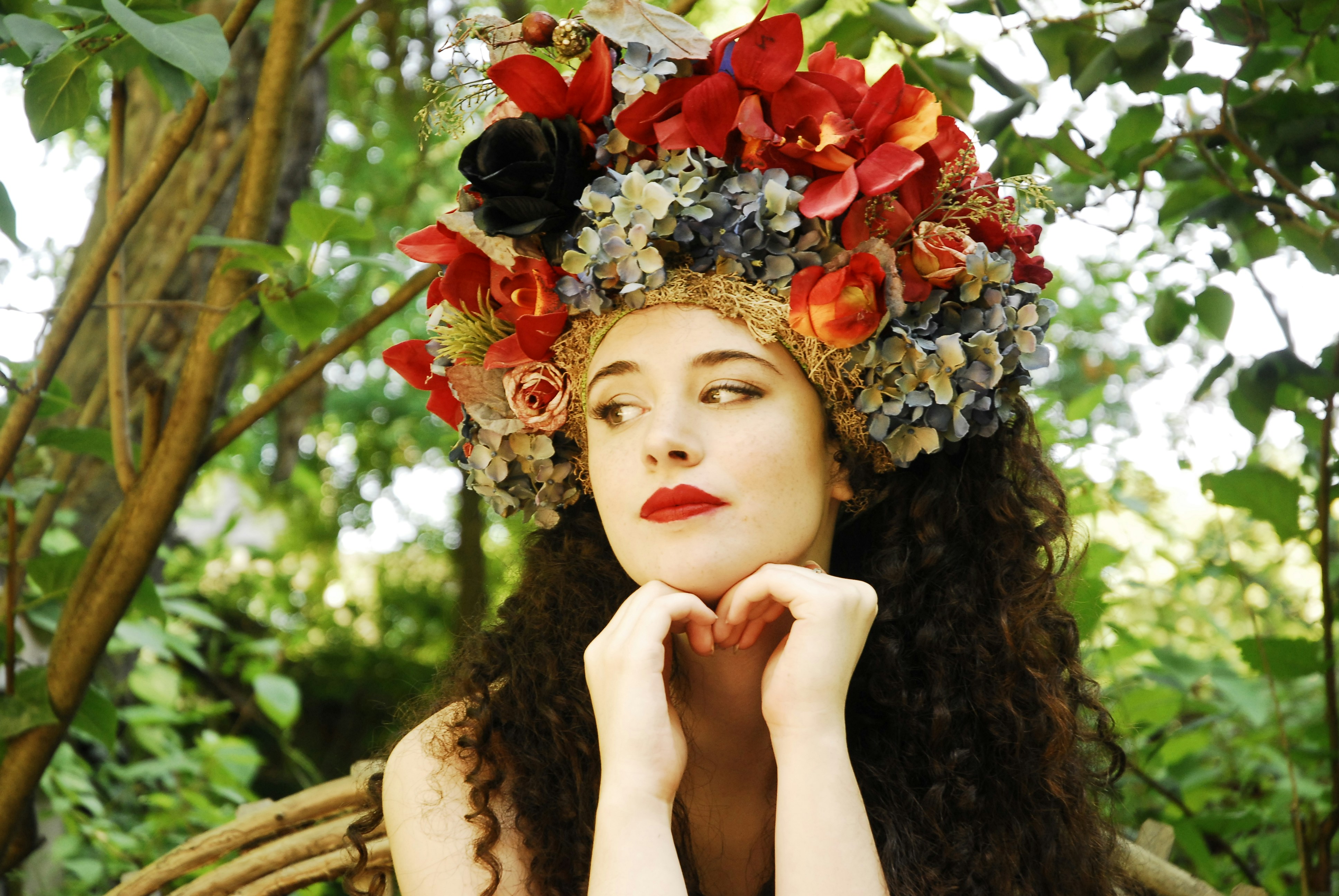 Person adorned with a vibrant flower crown, surrounded by lush greenery.