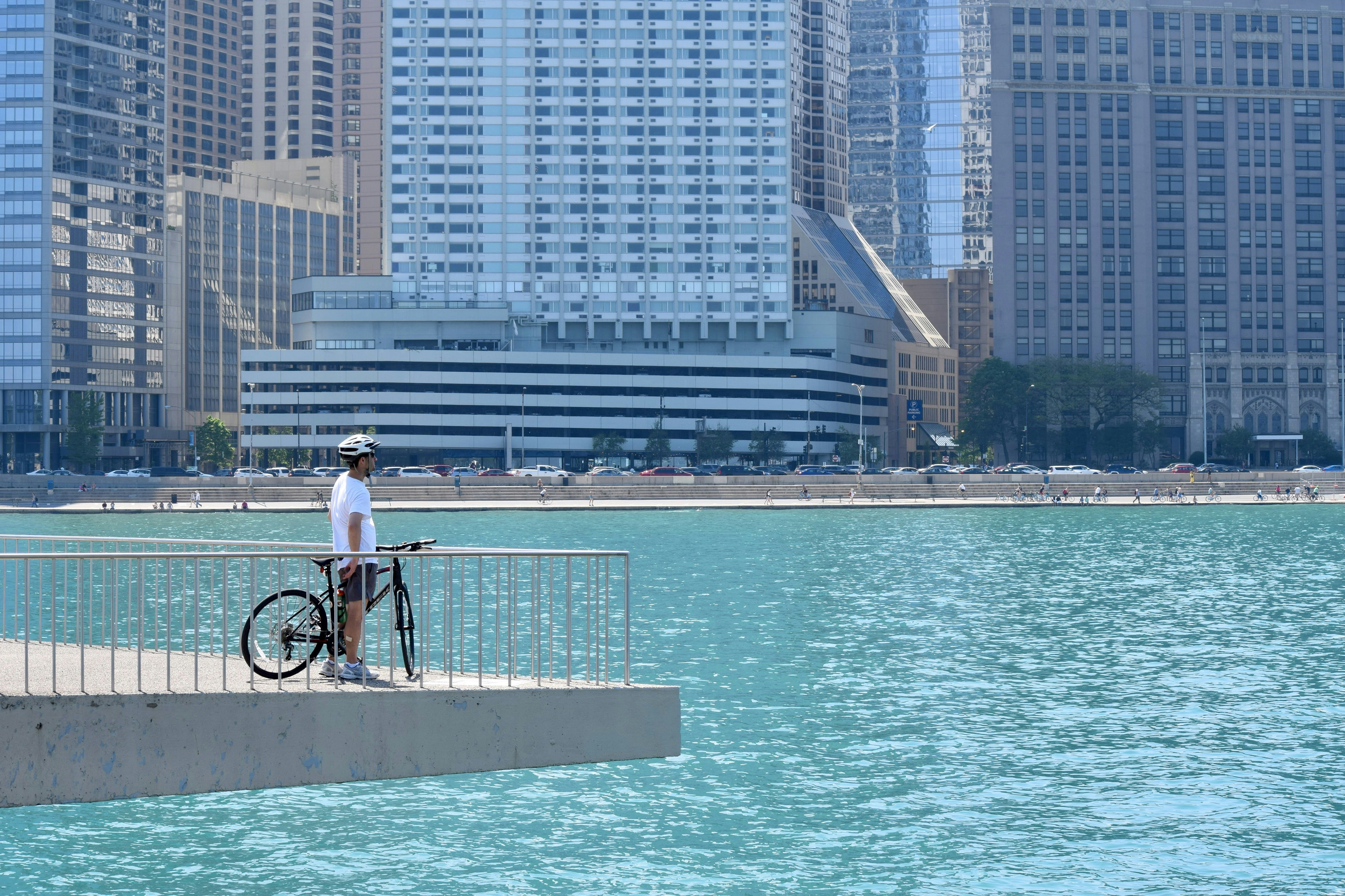 Harbor-side Pause: Cyclist and Bike Against Turquoise Water and a City Skyline