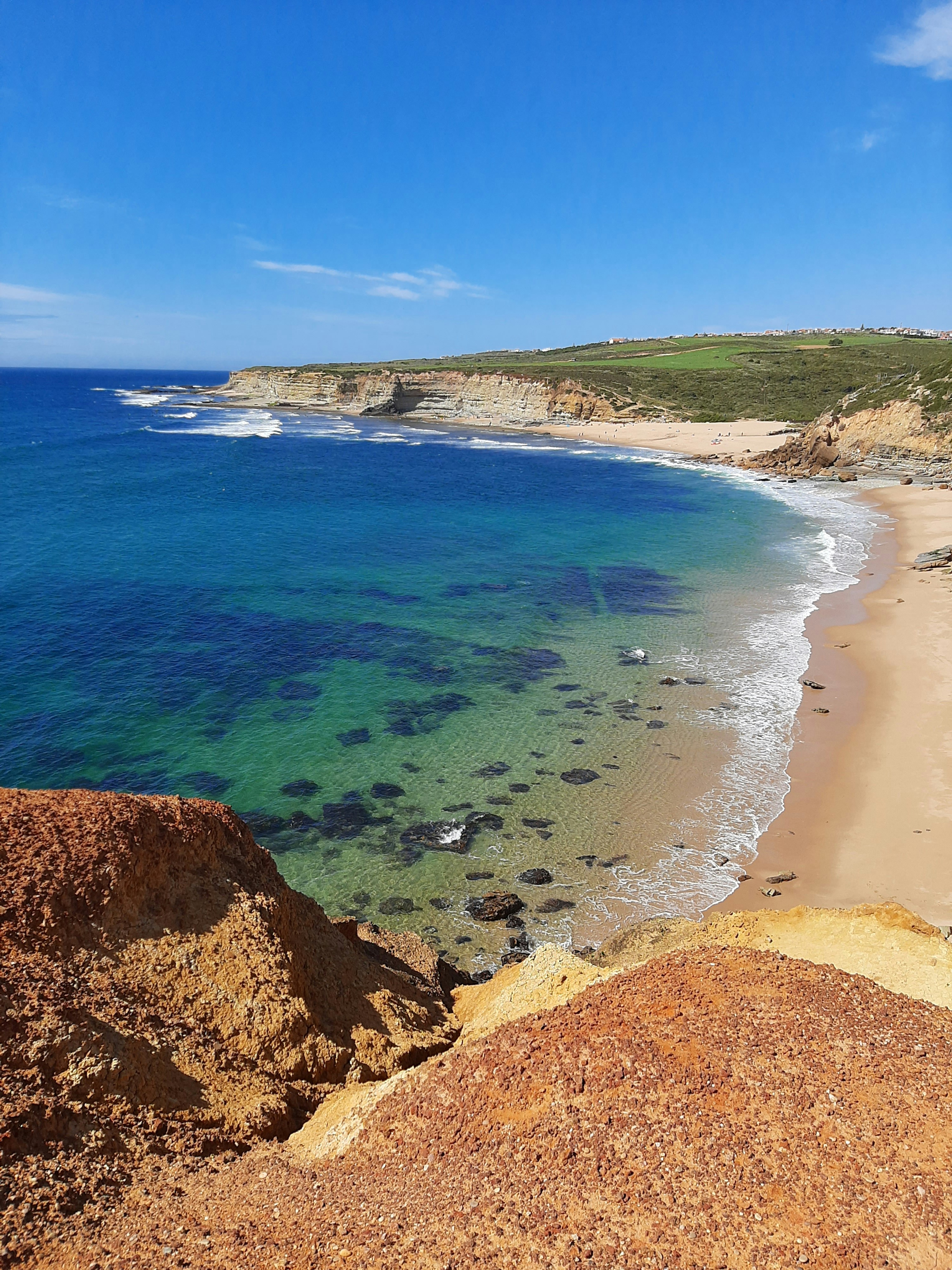 Vibrant shoreline with clear turquoise waters gently lapping against sandy beaches and rocky cliffs under a bright blue sky.