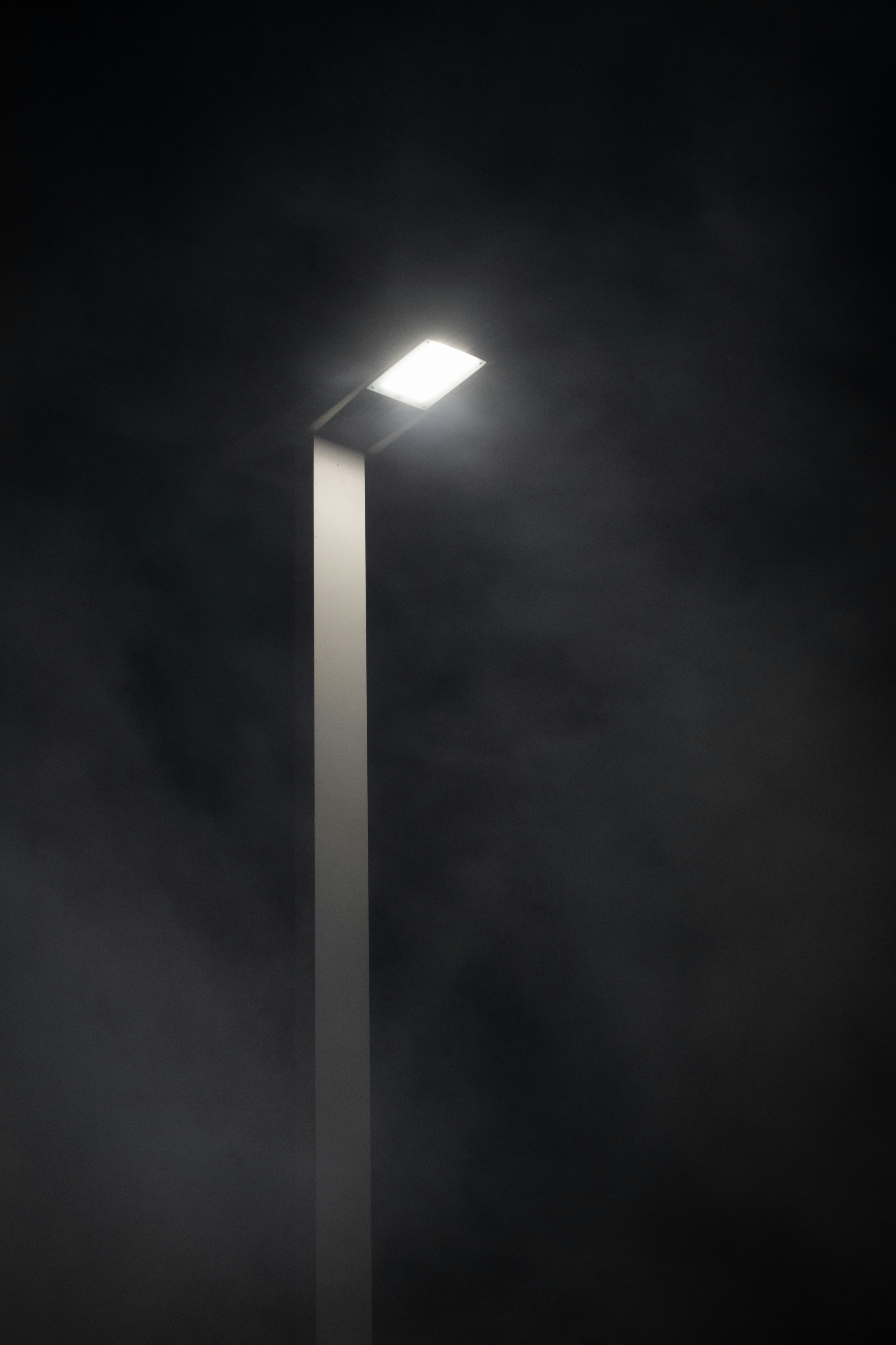 A street lamp stands tall amidst a swirling fog, casting a soft glow against a dark backdrop.