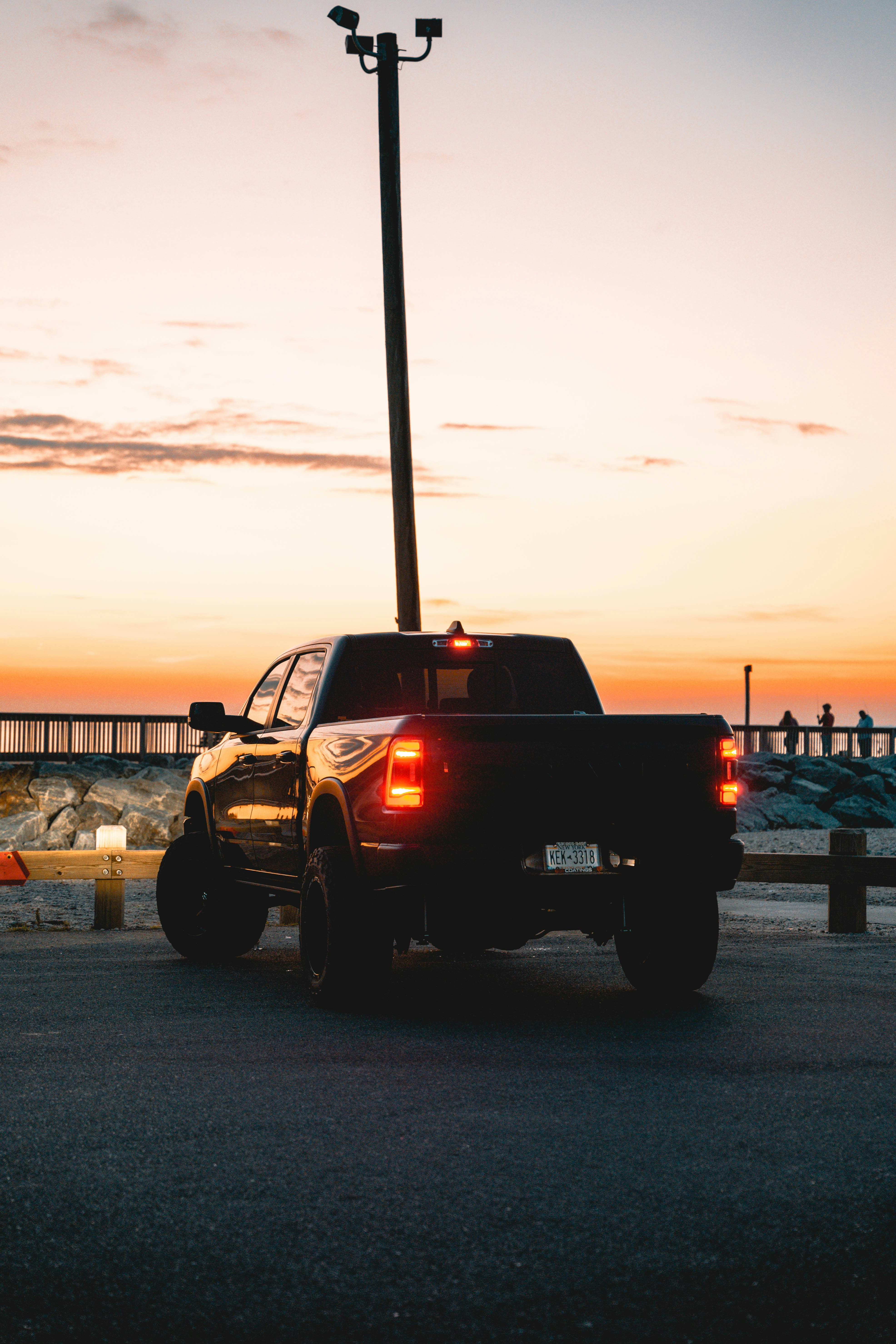 Black pickup truck parked near a shoreline at sunset, casting a silhouette against the vibrant sky. The scene captures the essence of adventure and tranquility.