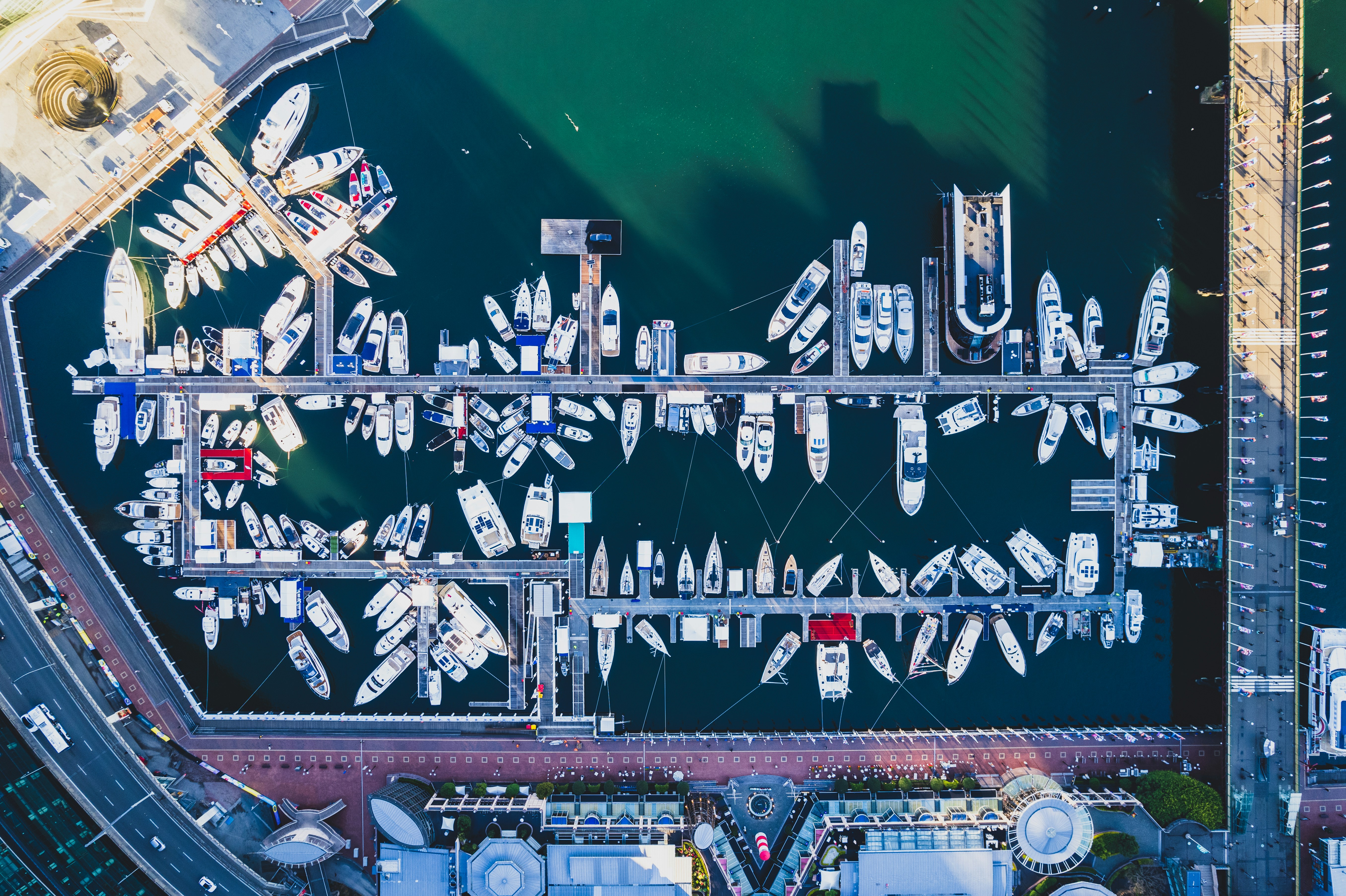 Aerial view of a marina filled with various yachts and boats arranged in a harmonious layout. The vibrant water contrasts beautifully with the vessels.