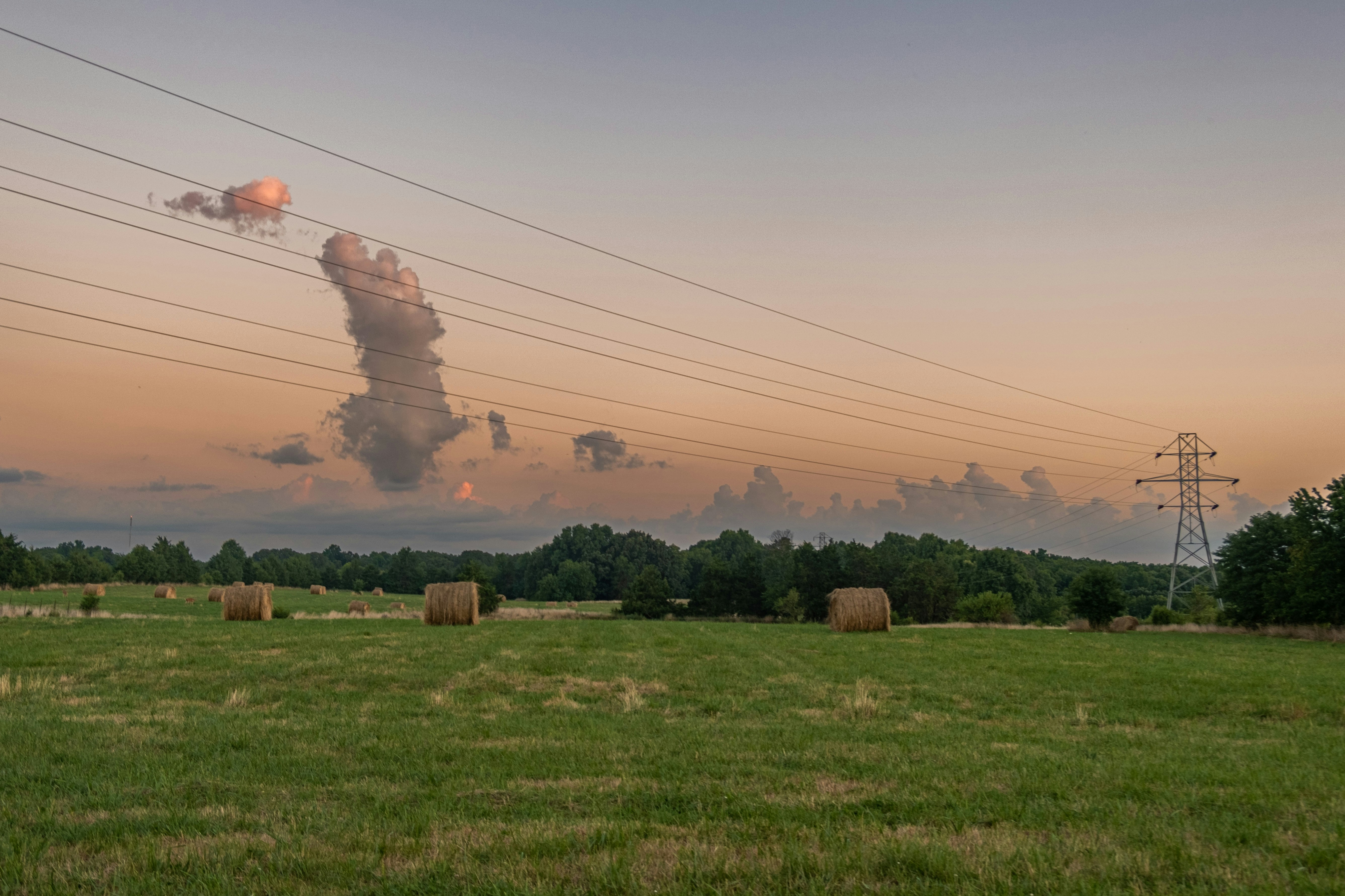 A field with hay bales and smoke stacks in the distance photo – Free ...