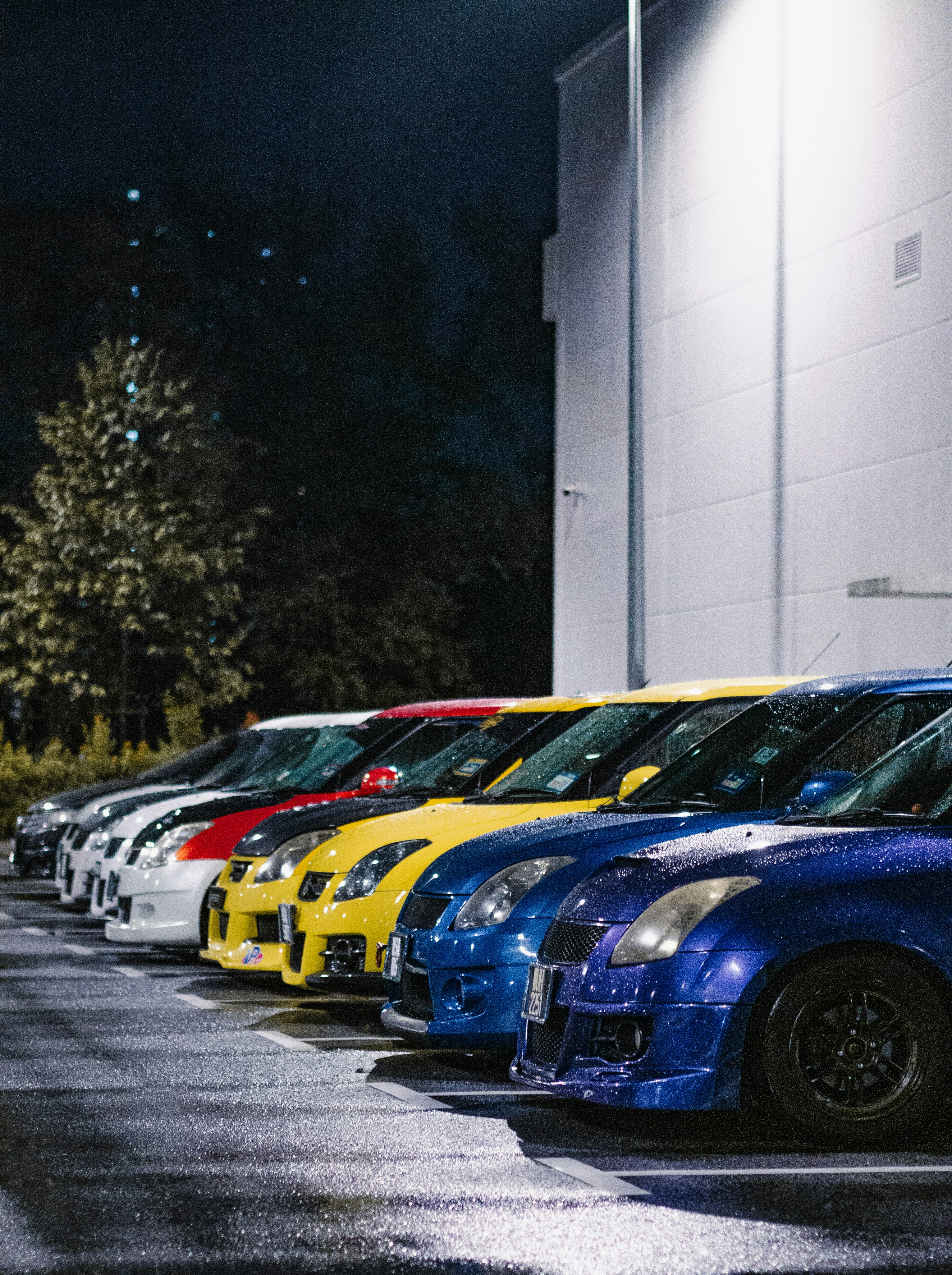 Midnight Parade of Colorful Cars Along a Rain-Slicked Wall