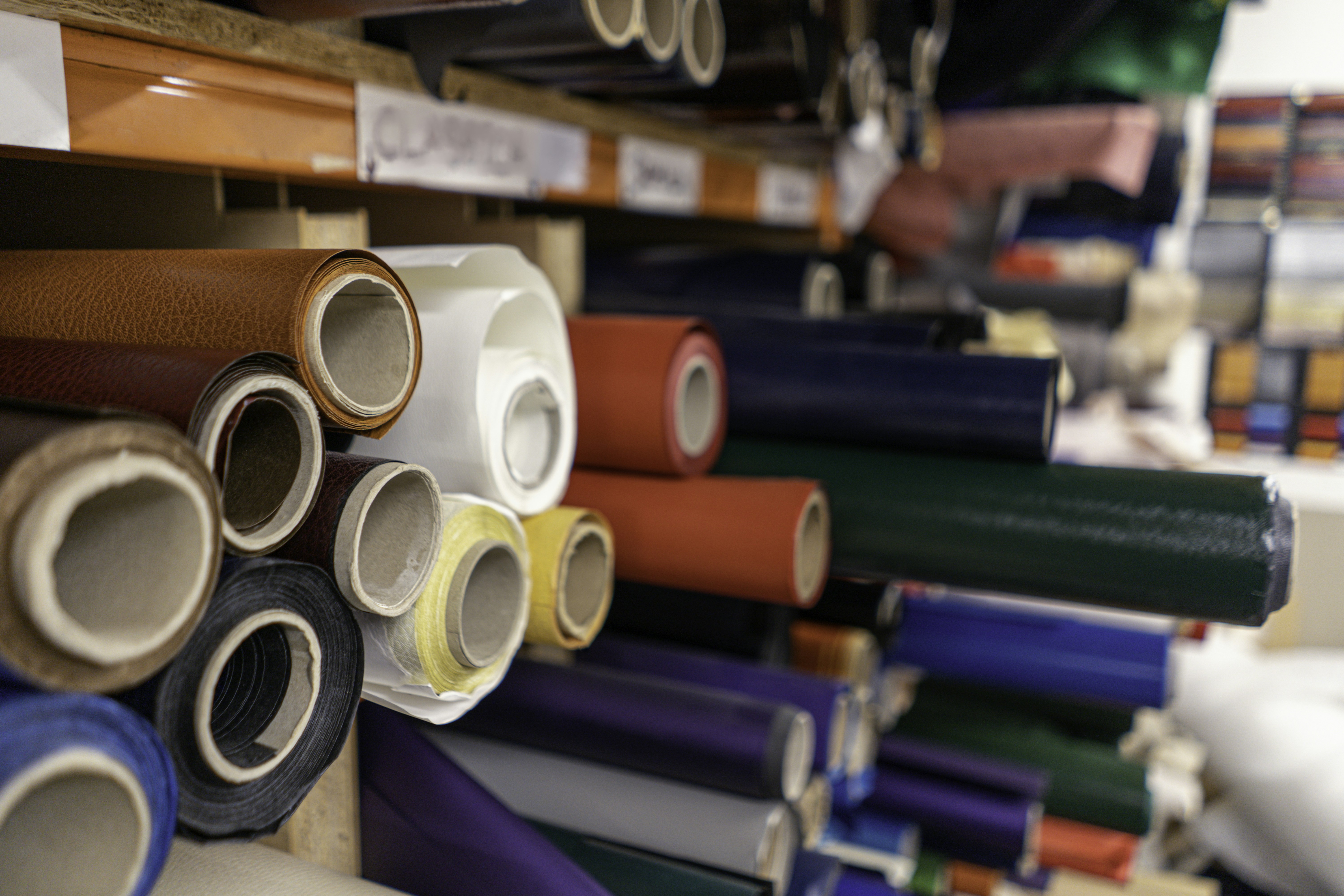 A vibrant display of rolled fabric and leather in various colors stacked on shelves, showcasing the diversity of textures and hues.