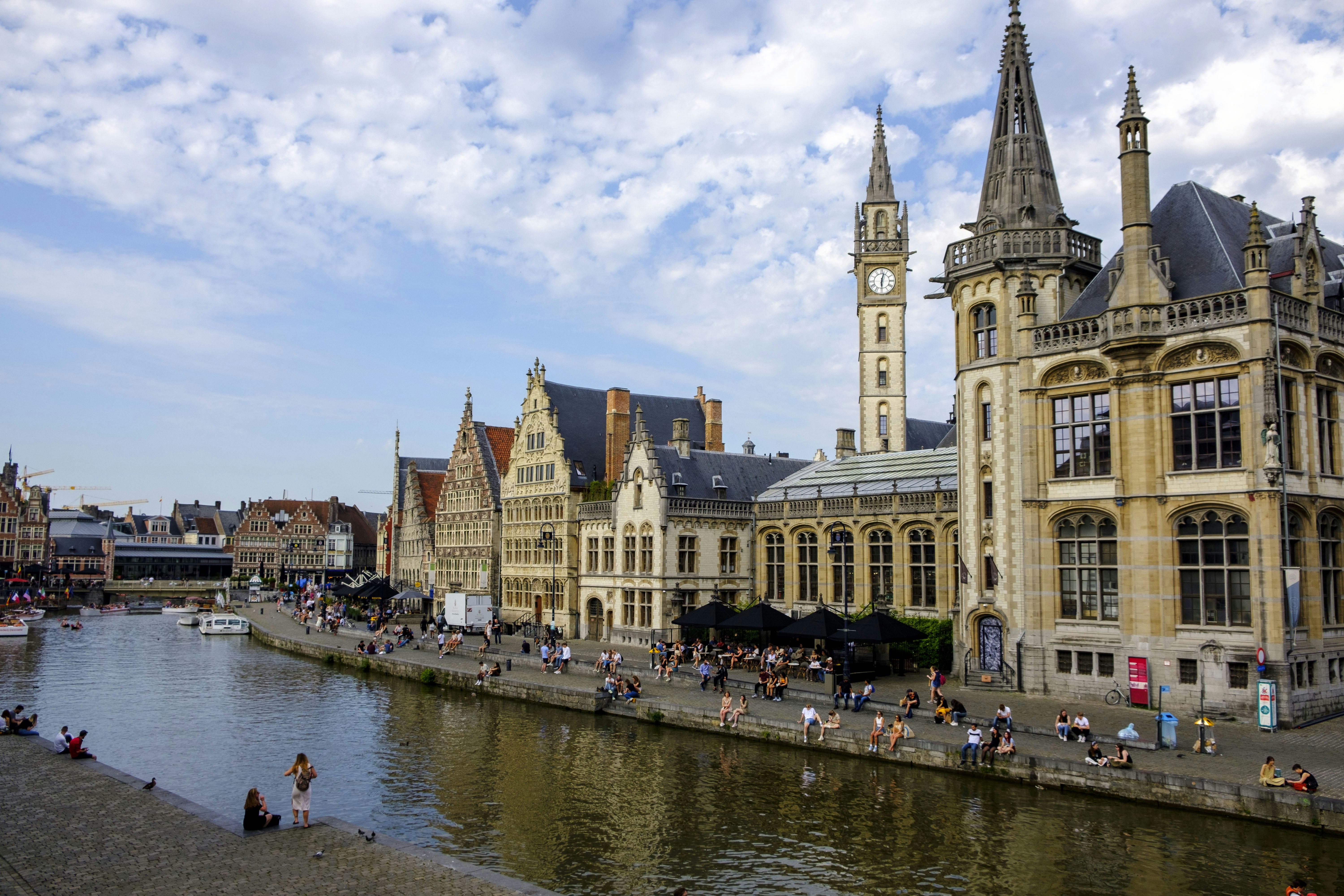 Historic European buildings line a riverbank under a blue sky with clouds.