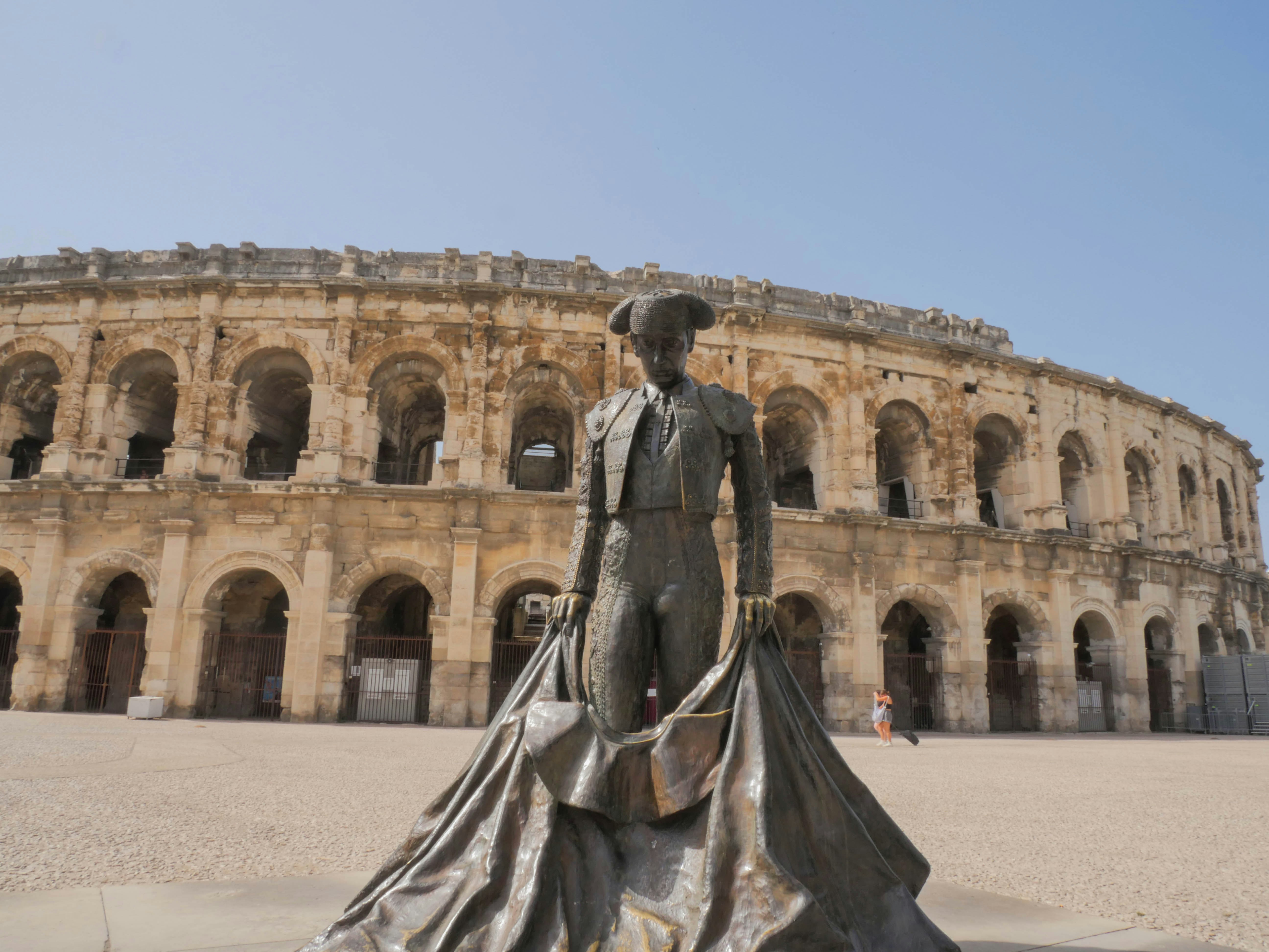 a statue of a person in front of a large building with El Djem in the background