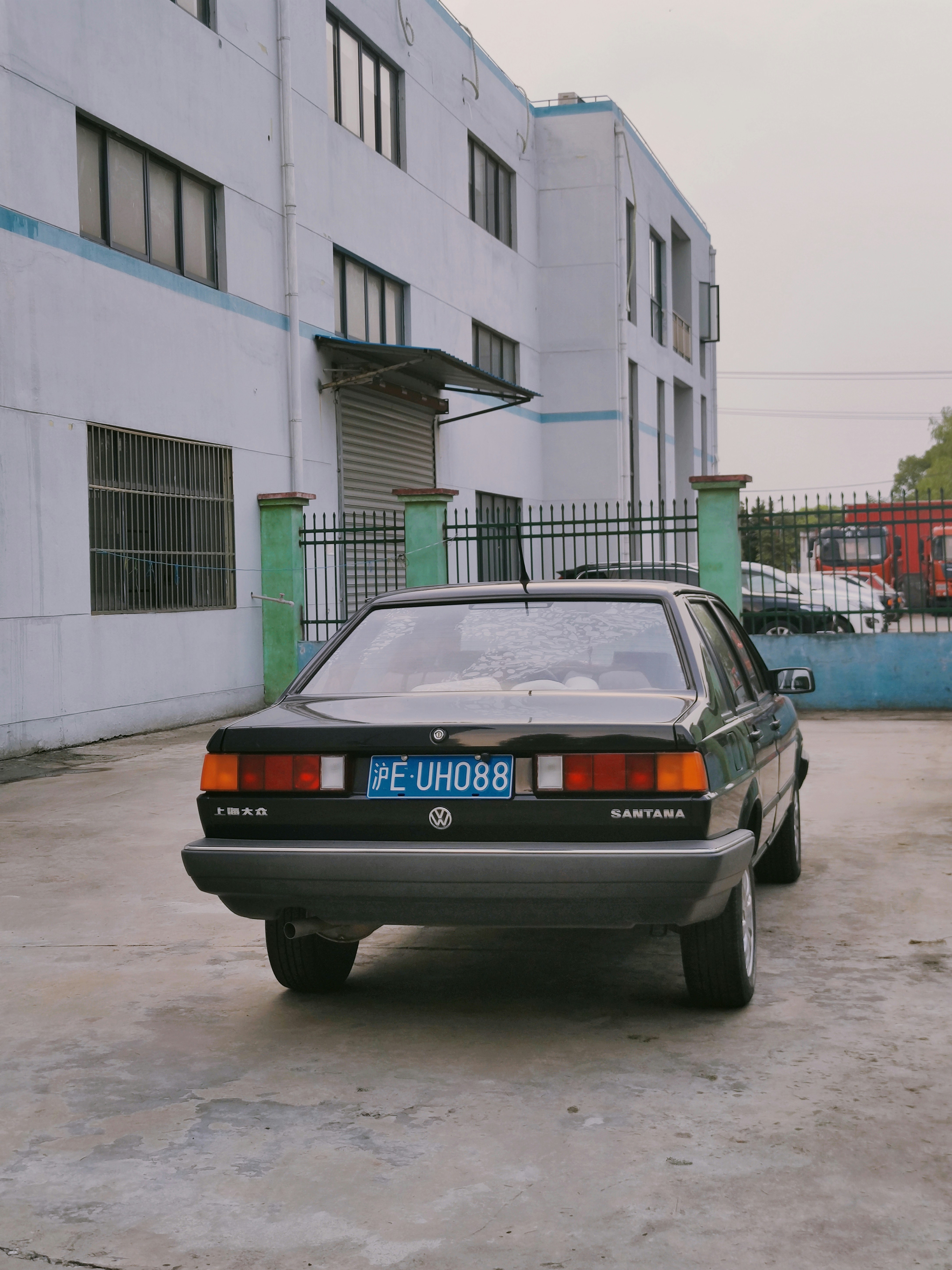 A black Volkswagen Santana parked in an industrial area, showcasing its retro design against a backdrop of modern architecture.