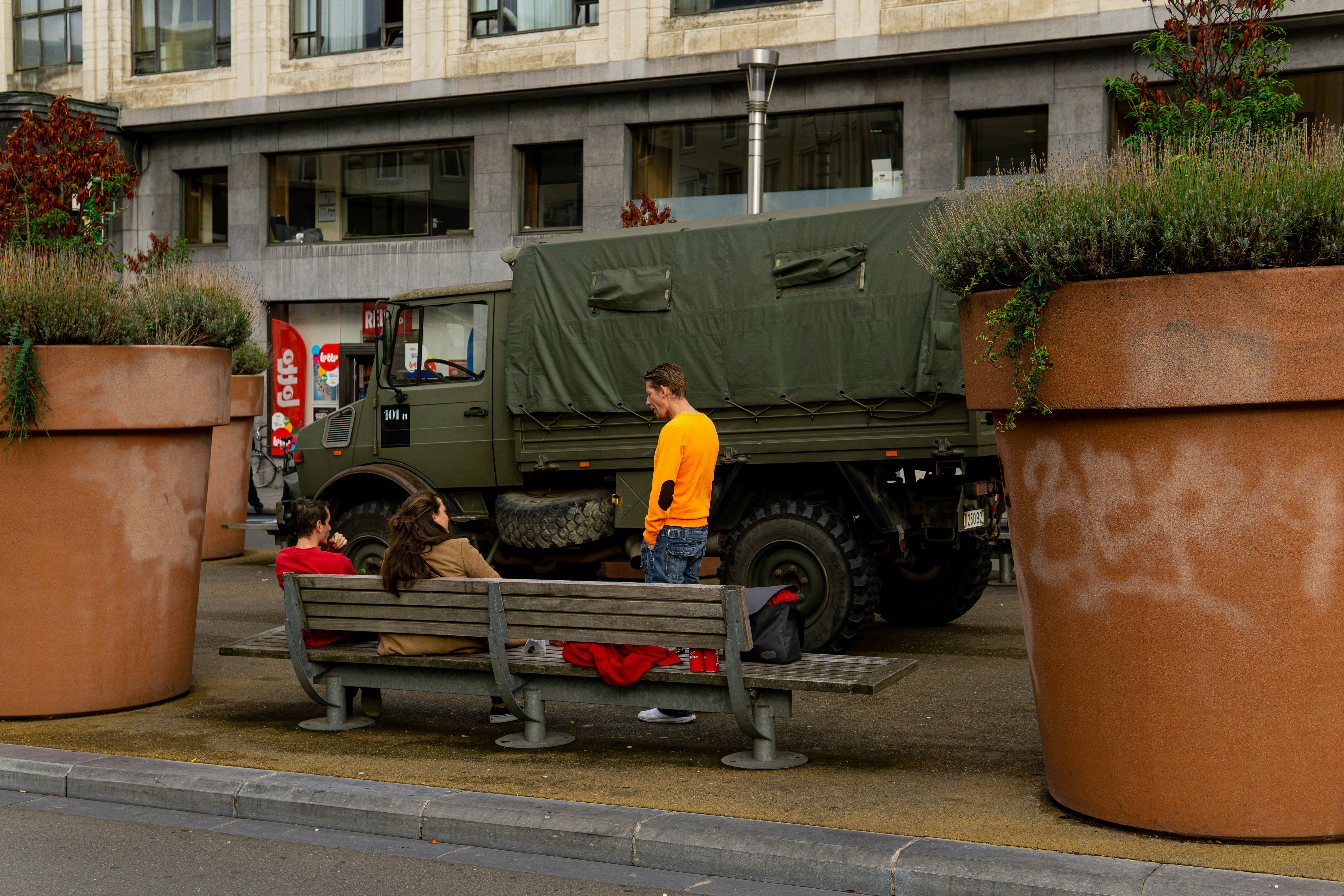 Urban Pause: Man in Orange among a Military Truck