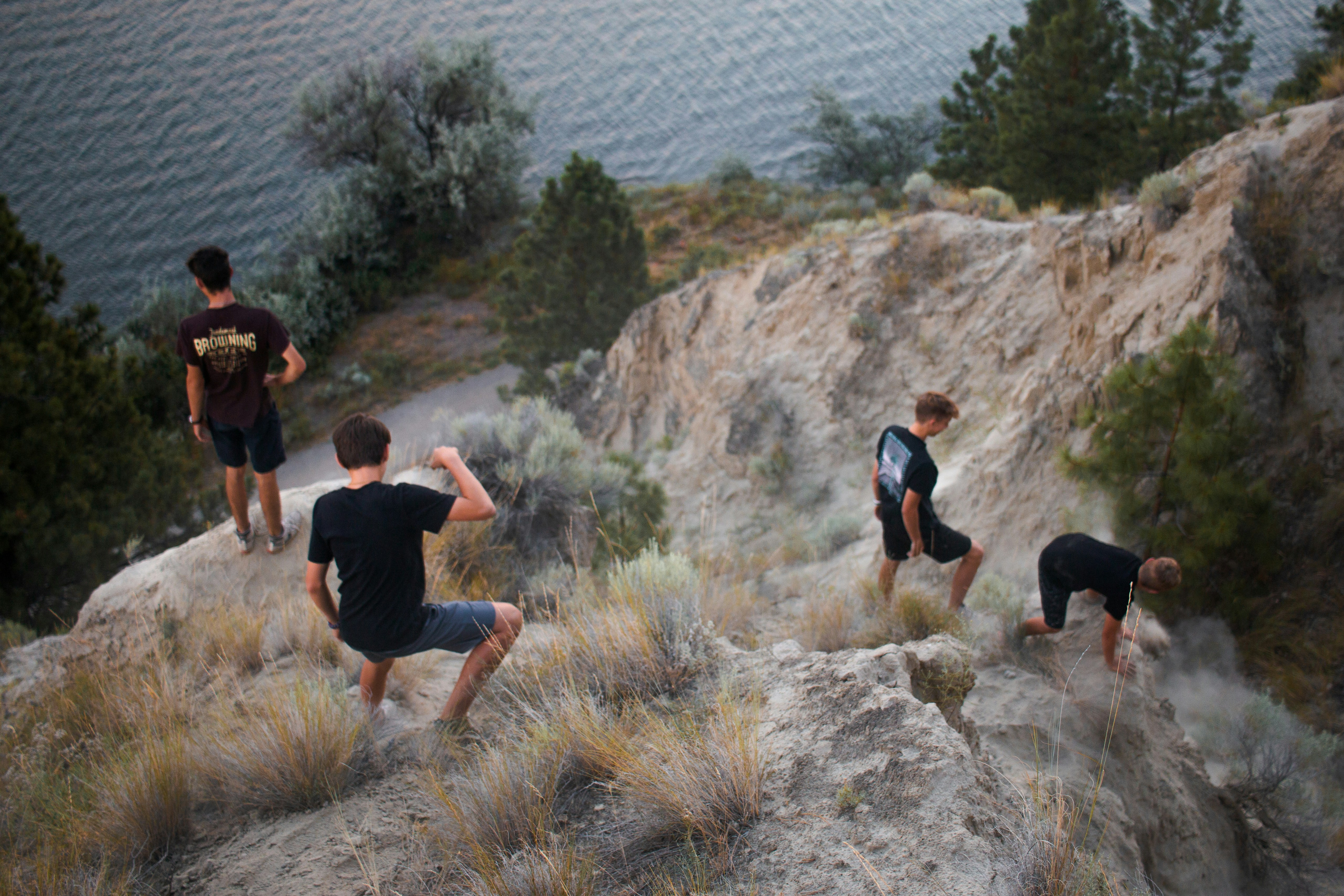Four people navigating a steep, rocky hillside with a lake in the background.