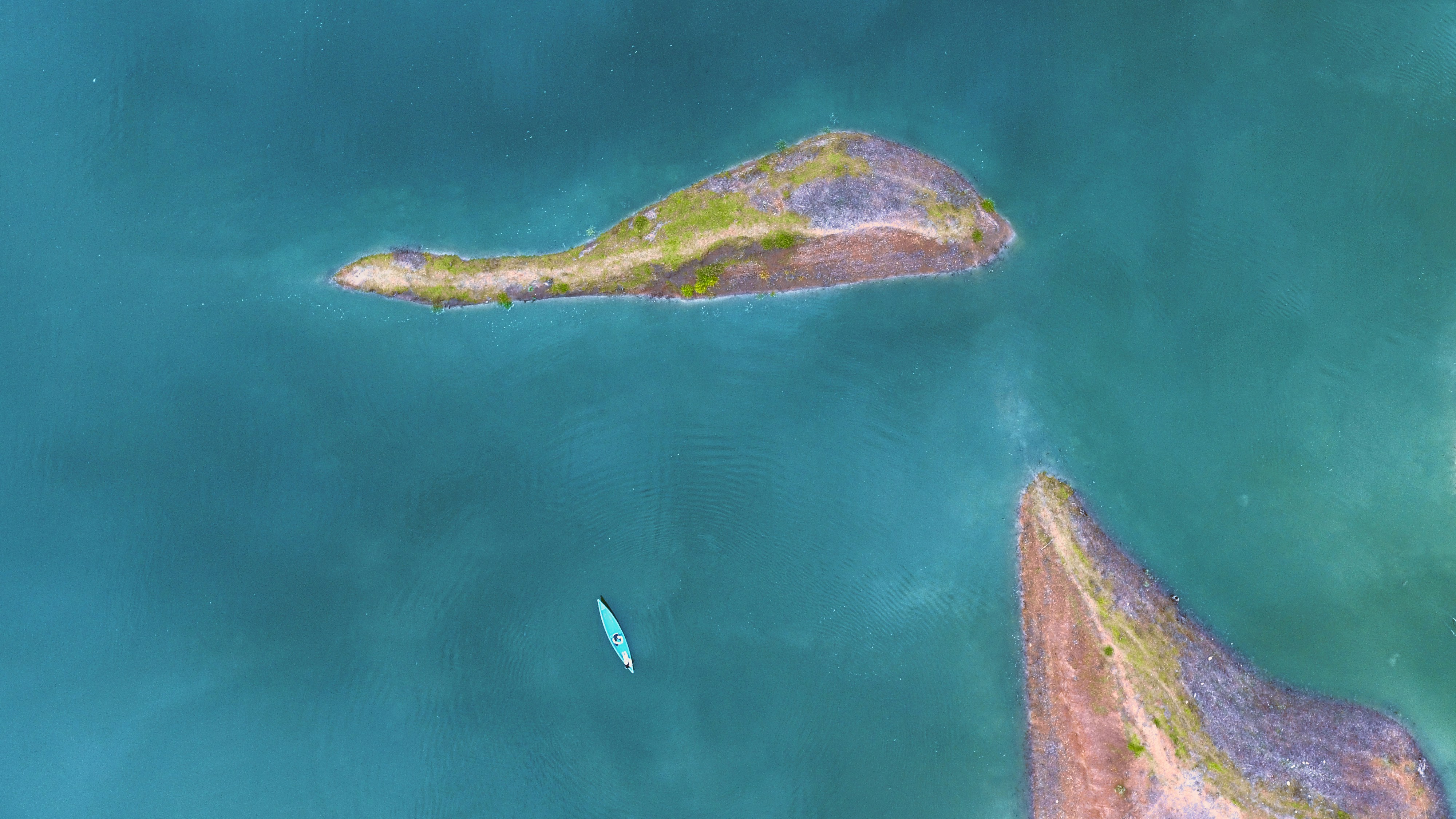 Lone Sailboat Skims a Teal Corridor Between Mossy Islets