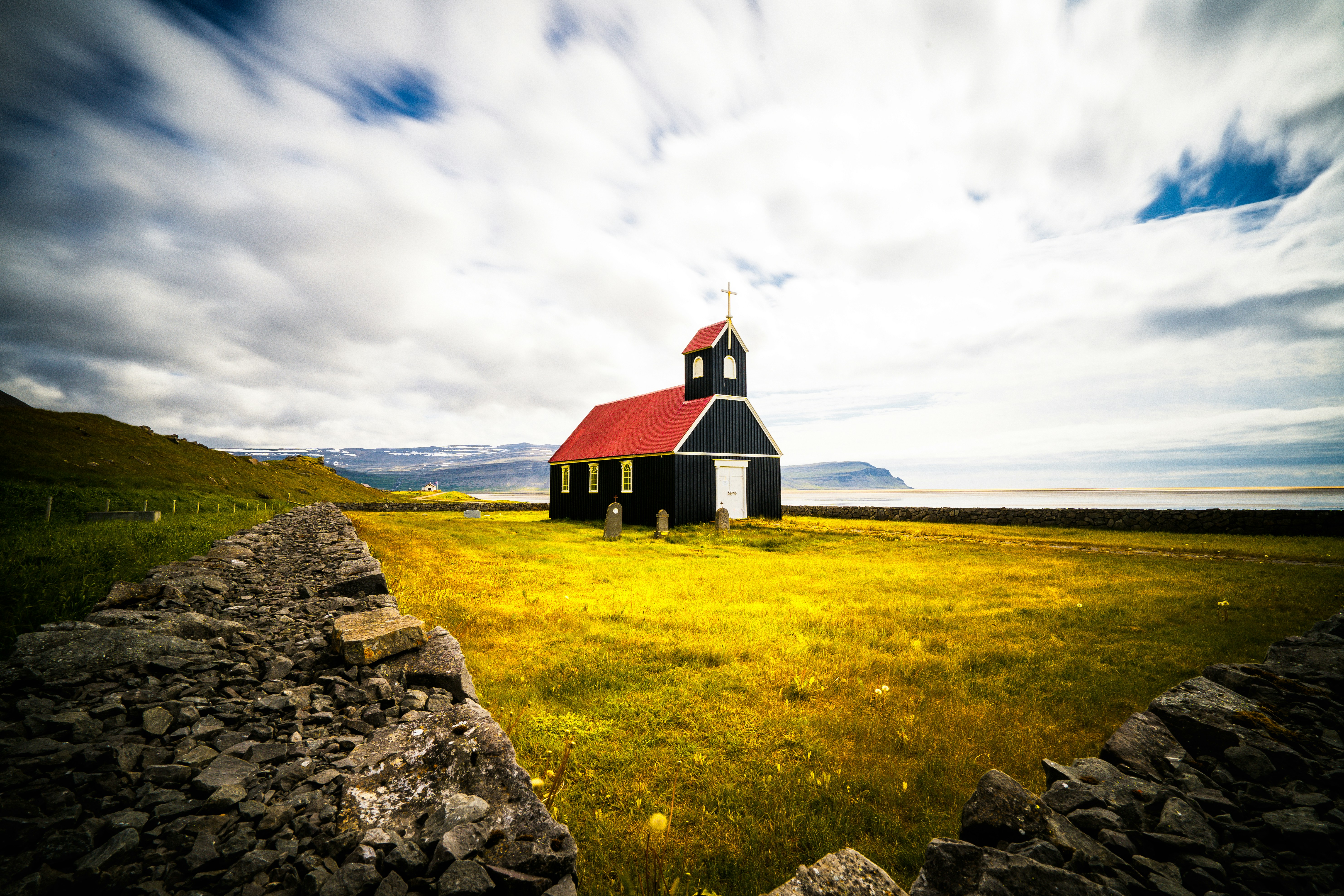 Red-roofed chapel on a windswept coast under a quilted sky
