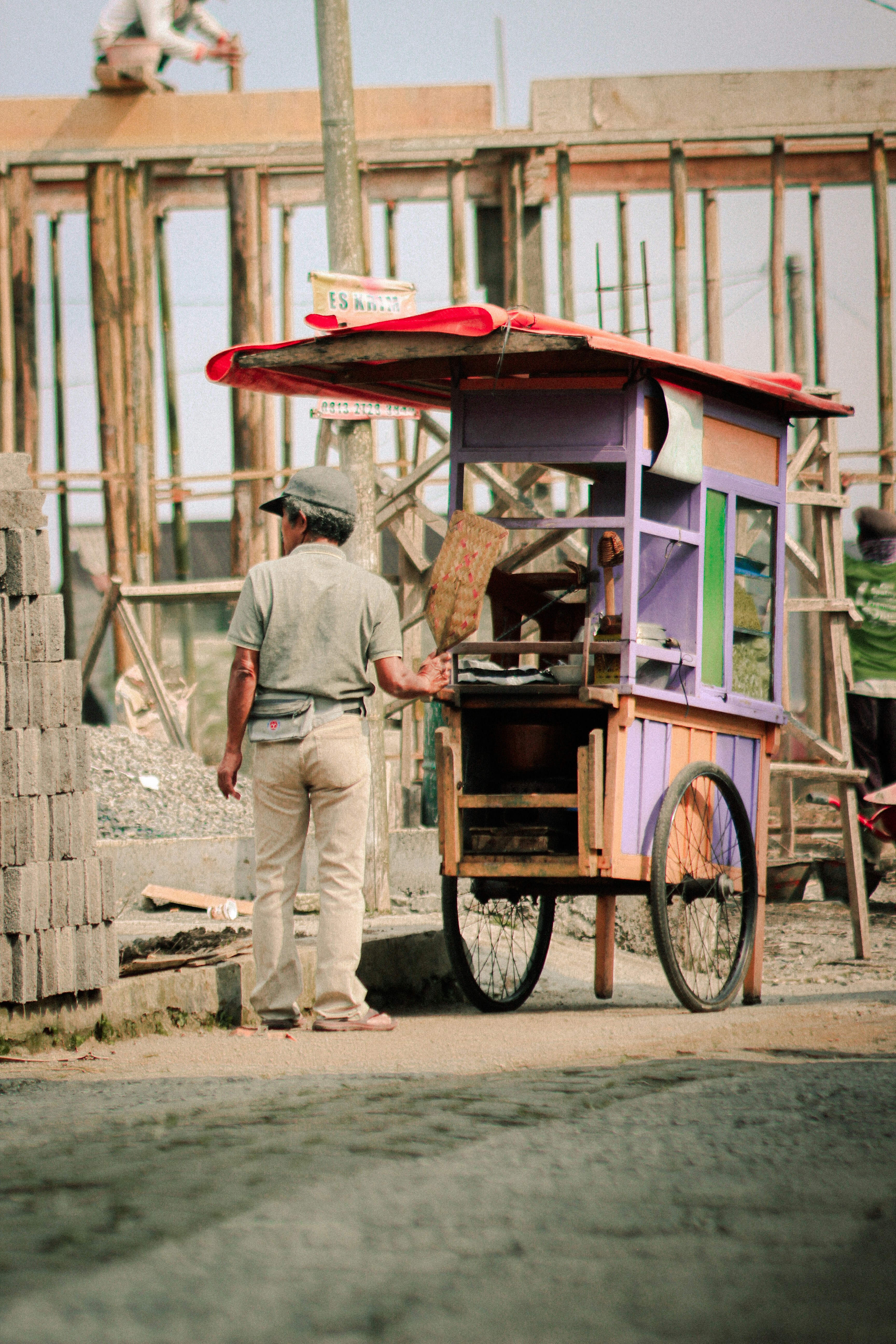 Vendor cart selling local delicacies on a bustling construction site, with workers engaged in building activities in the background.