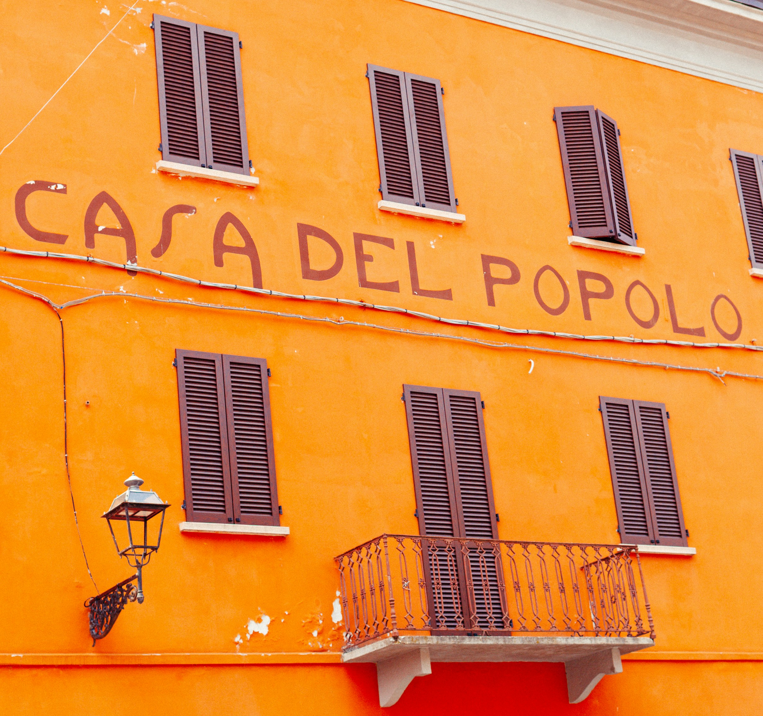 Sun-Washed Orange Facade with Balcony and Casa del Popolo Sign