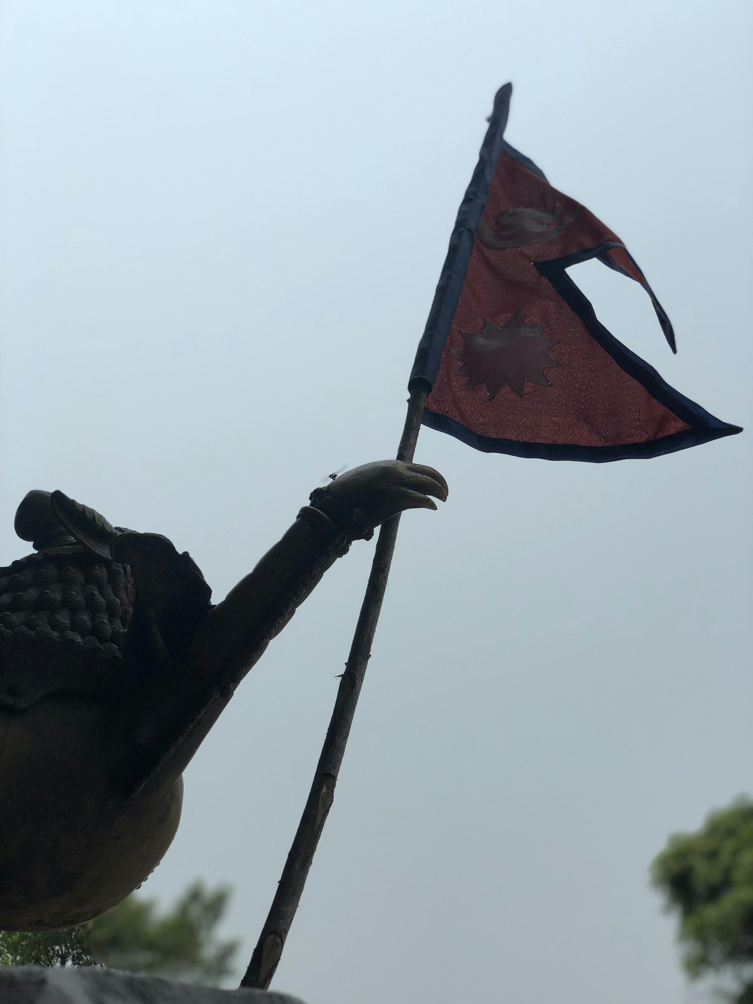 Statue of a lion holding a tattered Nepalese flag against a clear sky.