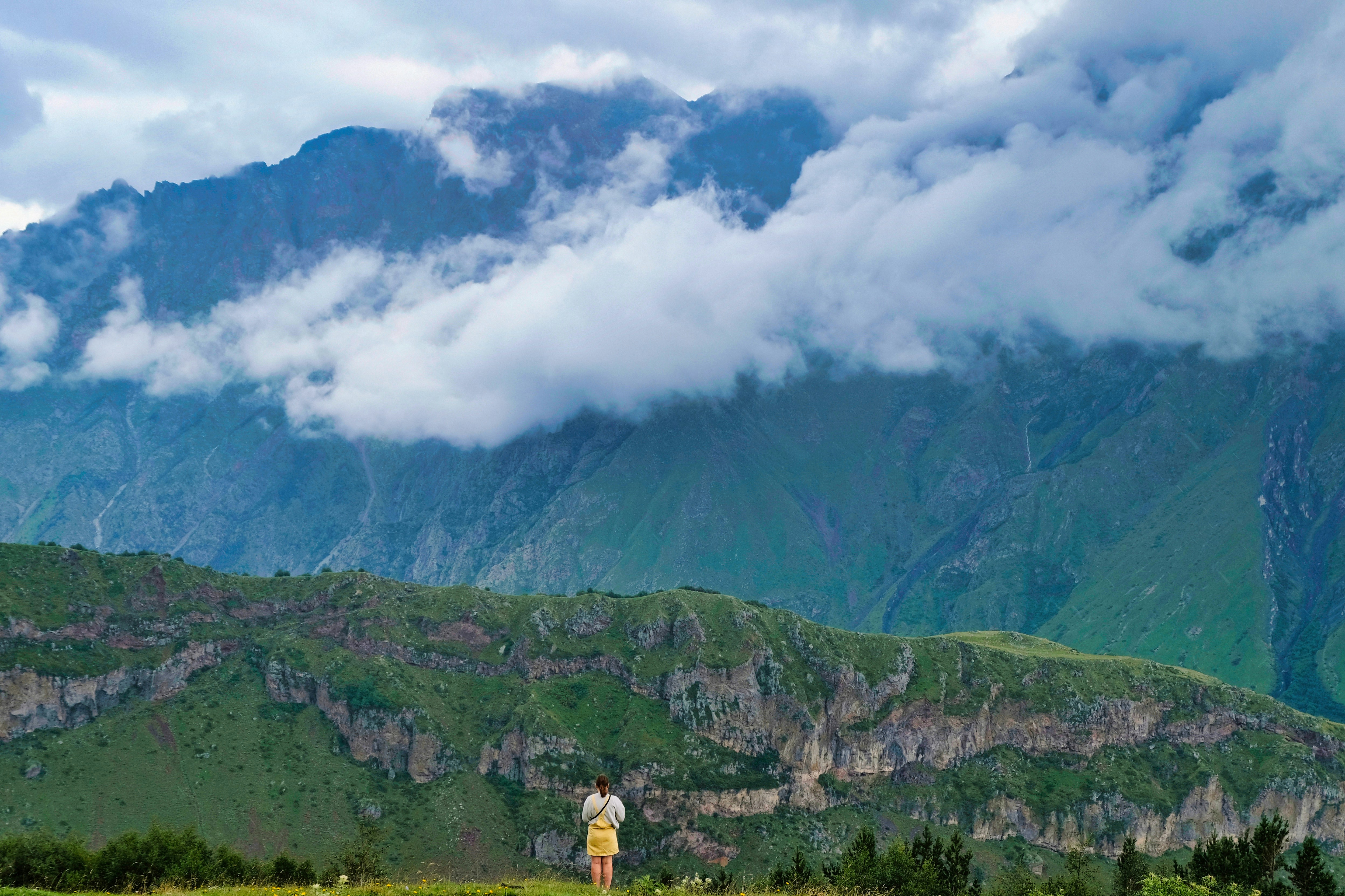 Hiker at the Foot of Veiled Peaks under a Cloud-Laden Sky